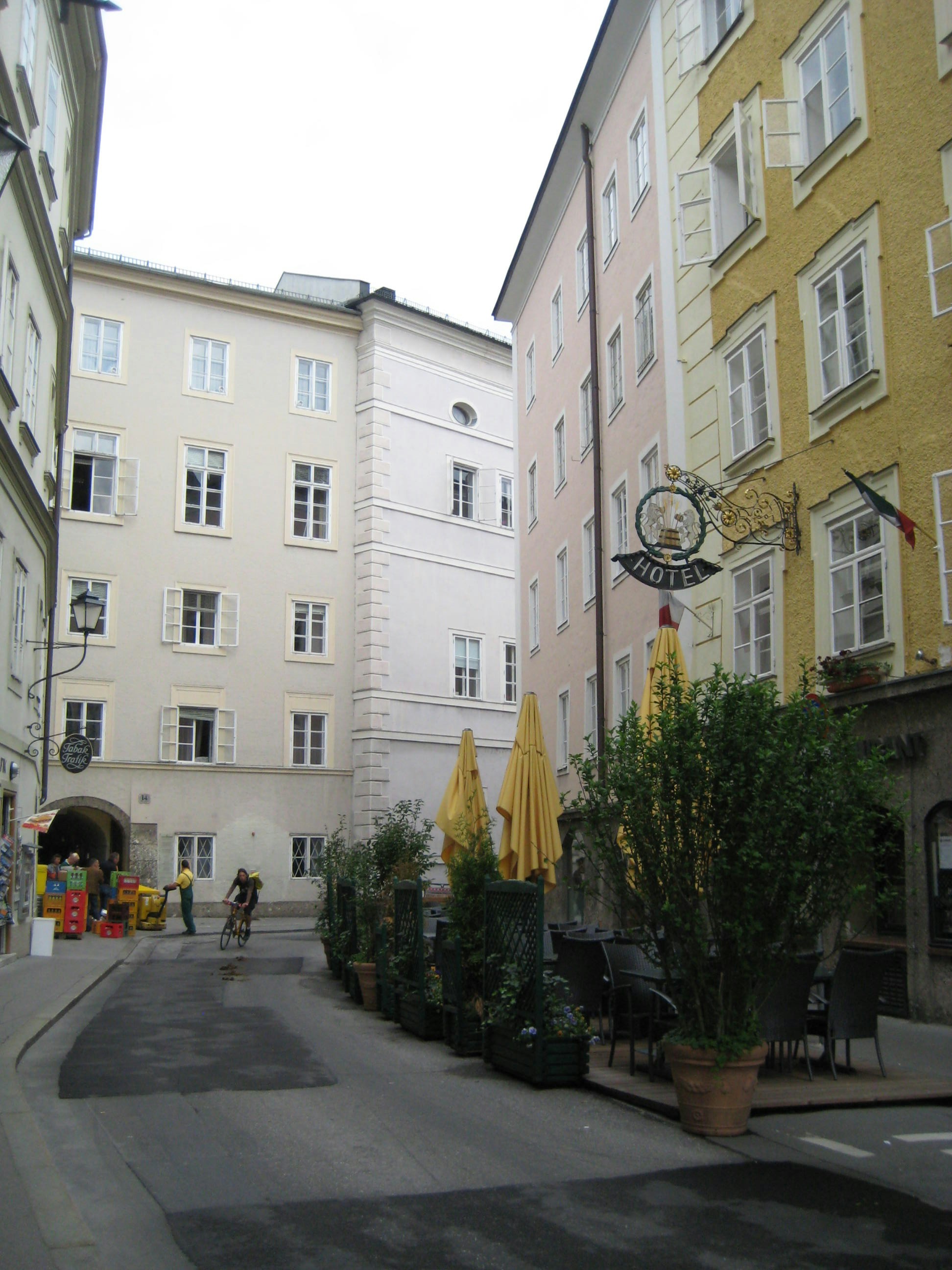 Quaint alleyway lined with potted plants and outdoor seating, showcasing the architectural charm of the surrounding buildings. Hotel sign hangs prominently above.