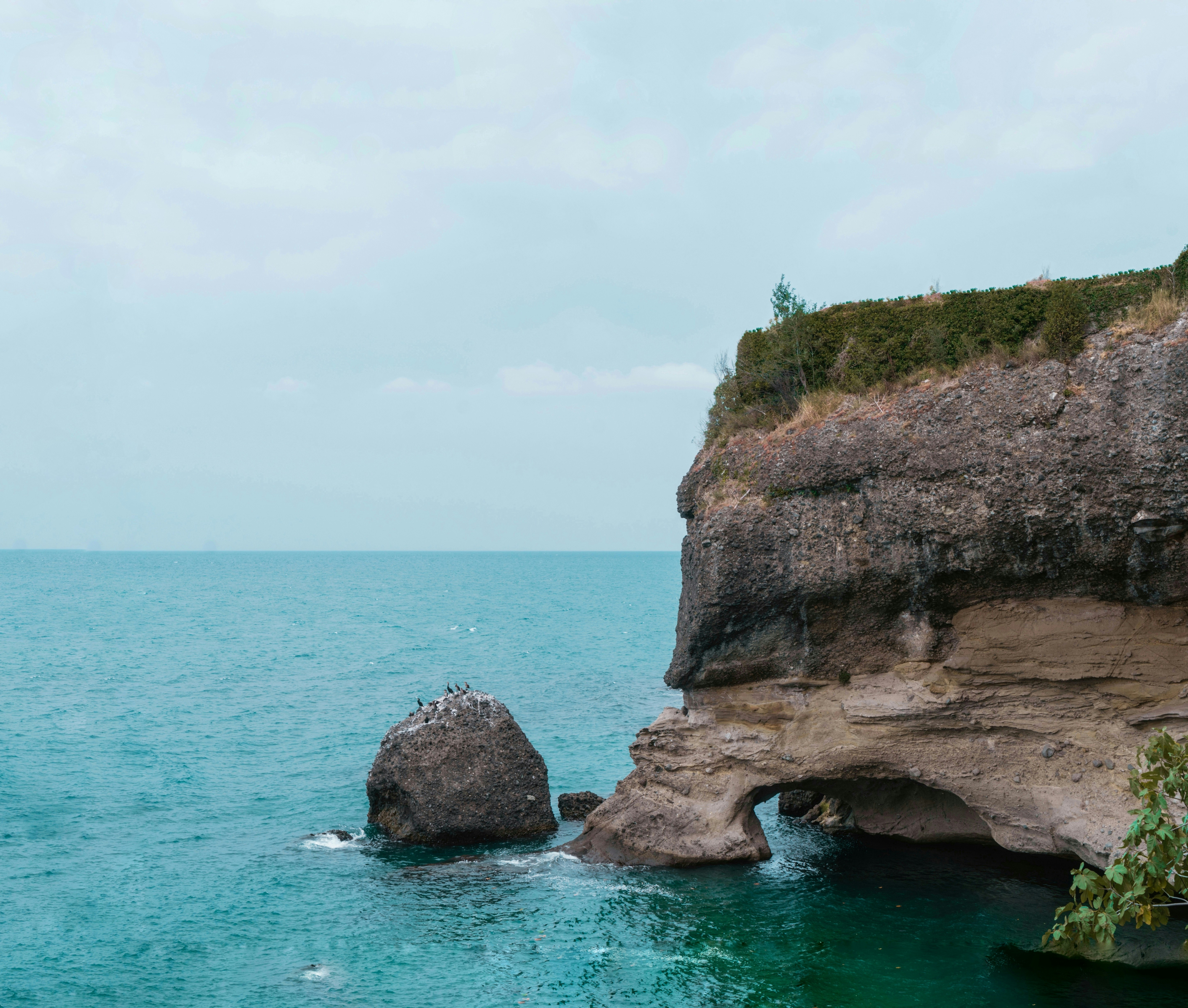 A large rock sticking out of the ocean next to a cliff photo – Free Sea ...