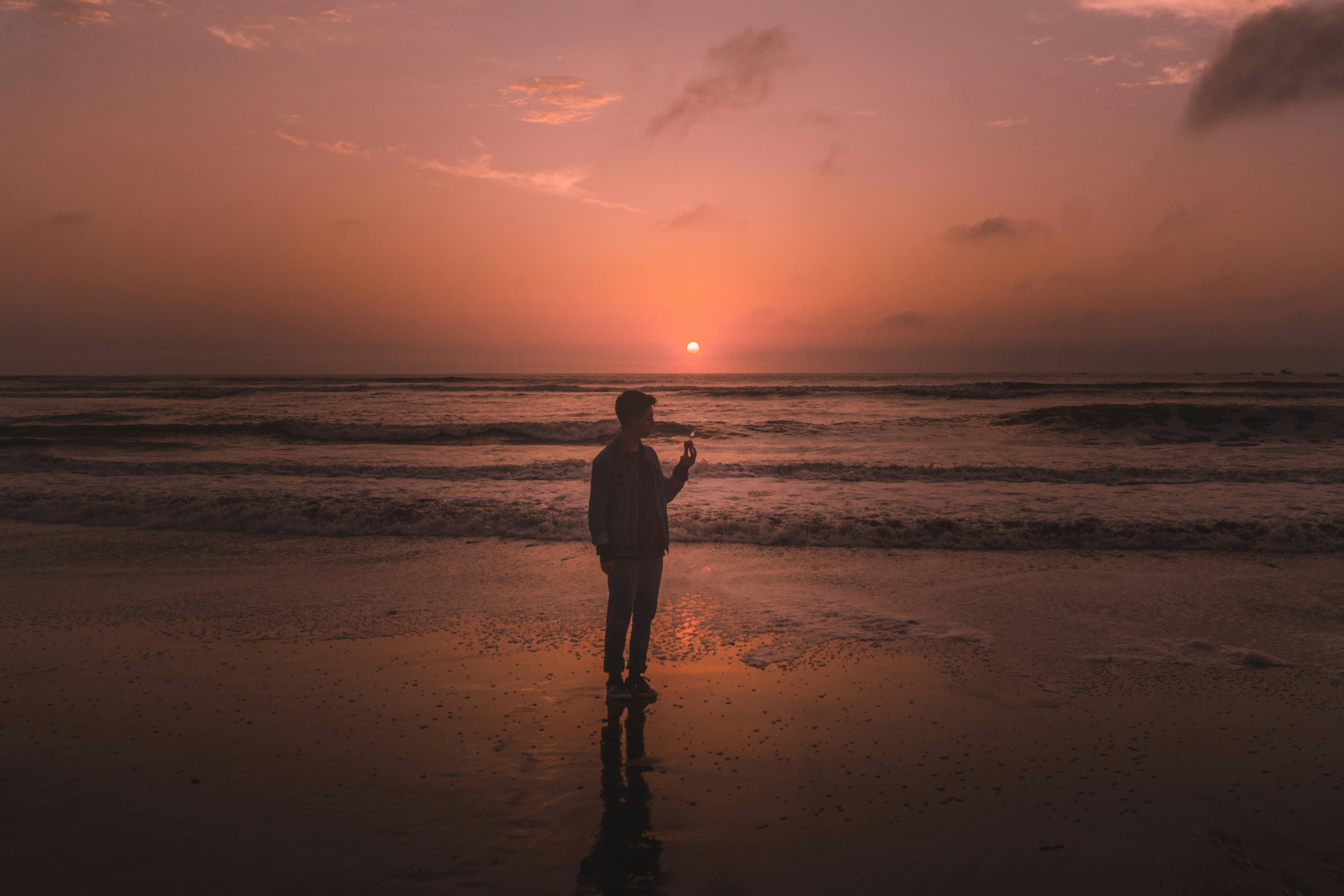 Silhouette of a person standing on a beach at sunset with waves in the background.