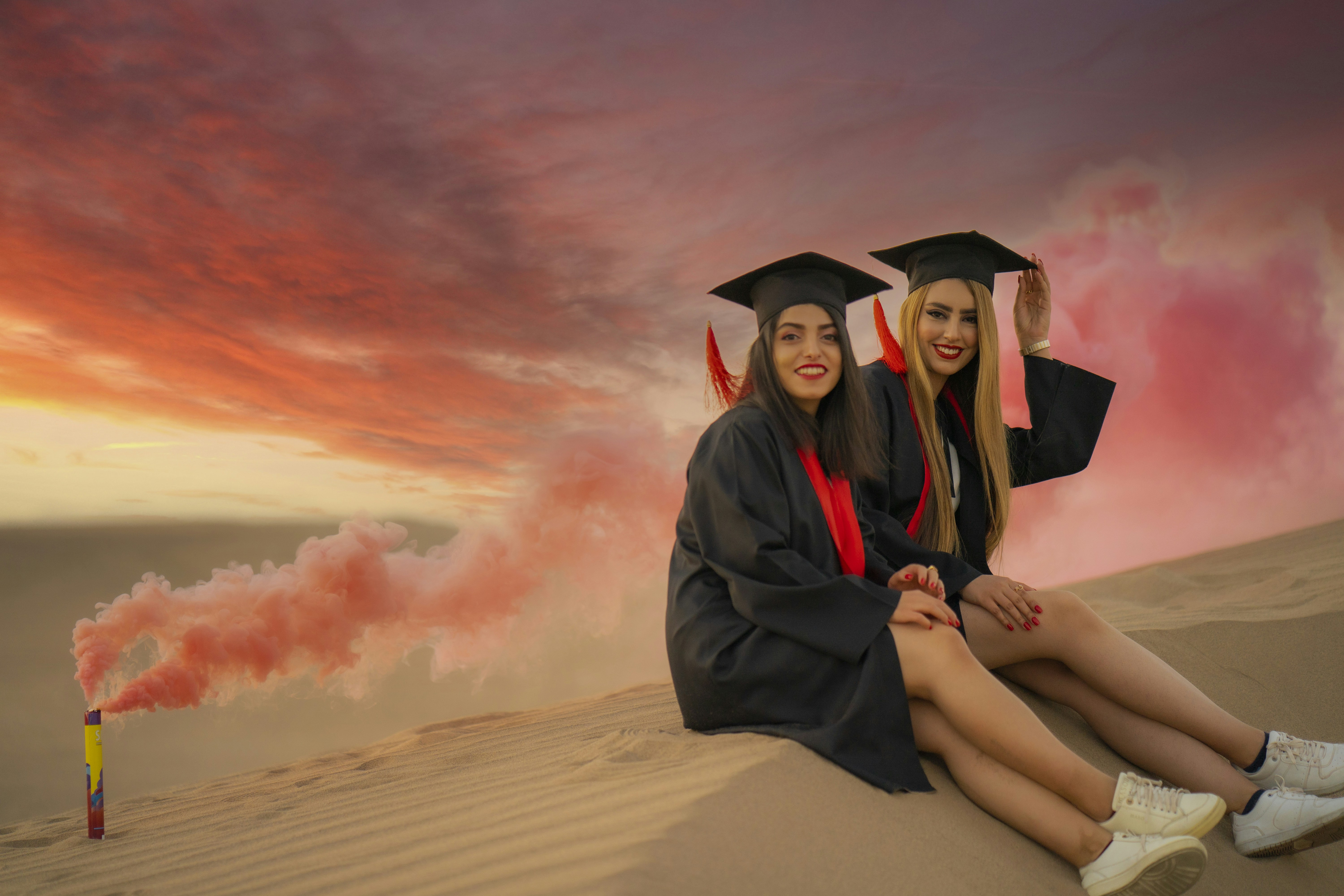 Two women in graduation gowns sitting on a sand dune photo – Free Iran ...