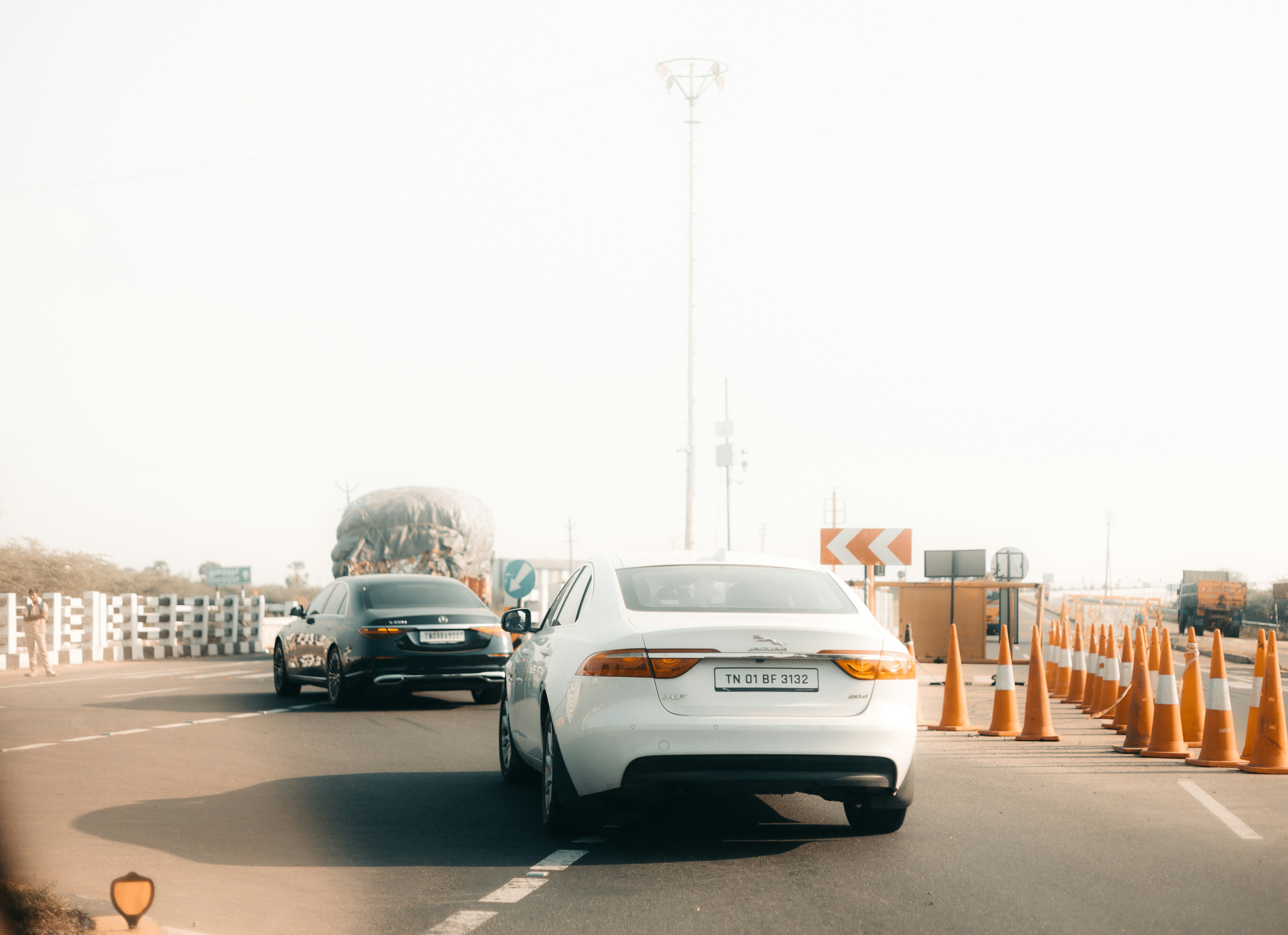 White car travels alongside traffic cones under bright daylight on a city road.