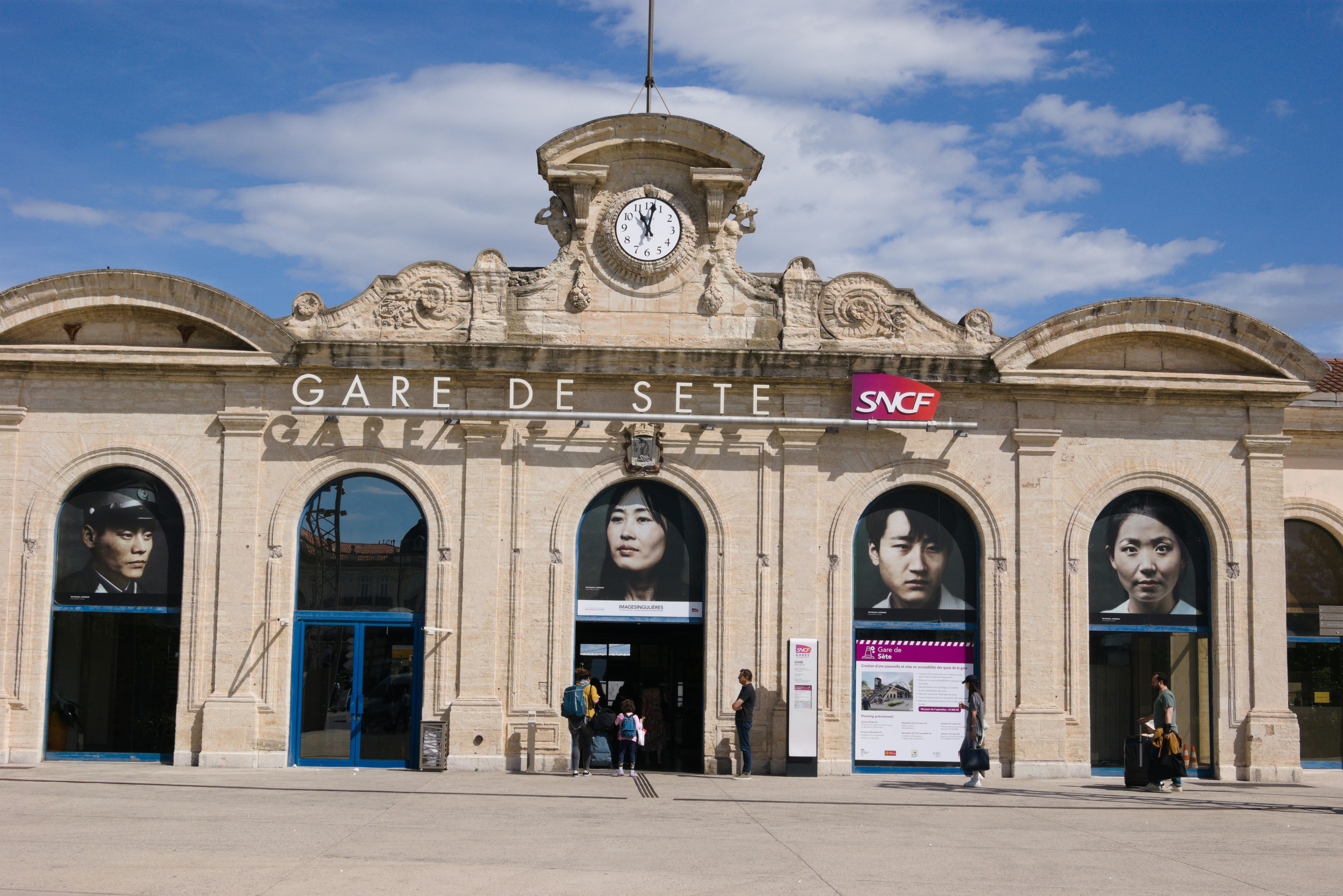 Historic train station entrance with a central clock under a clear blue sky.