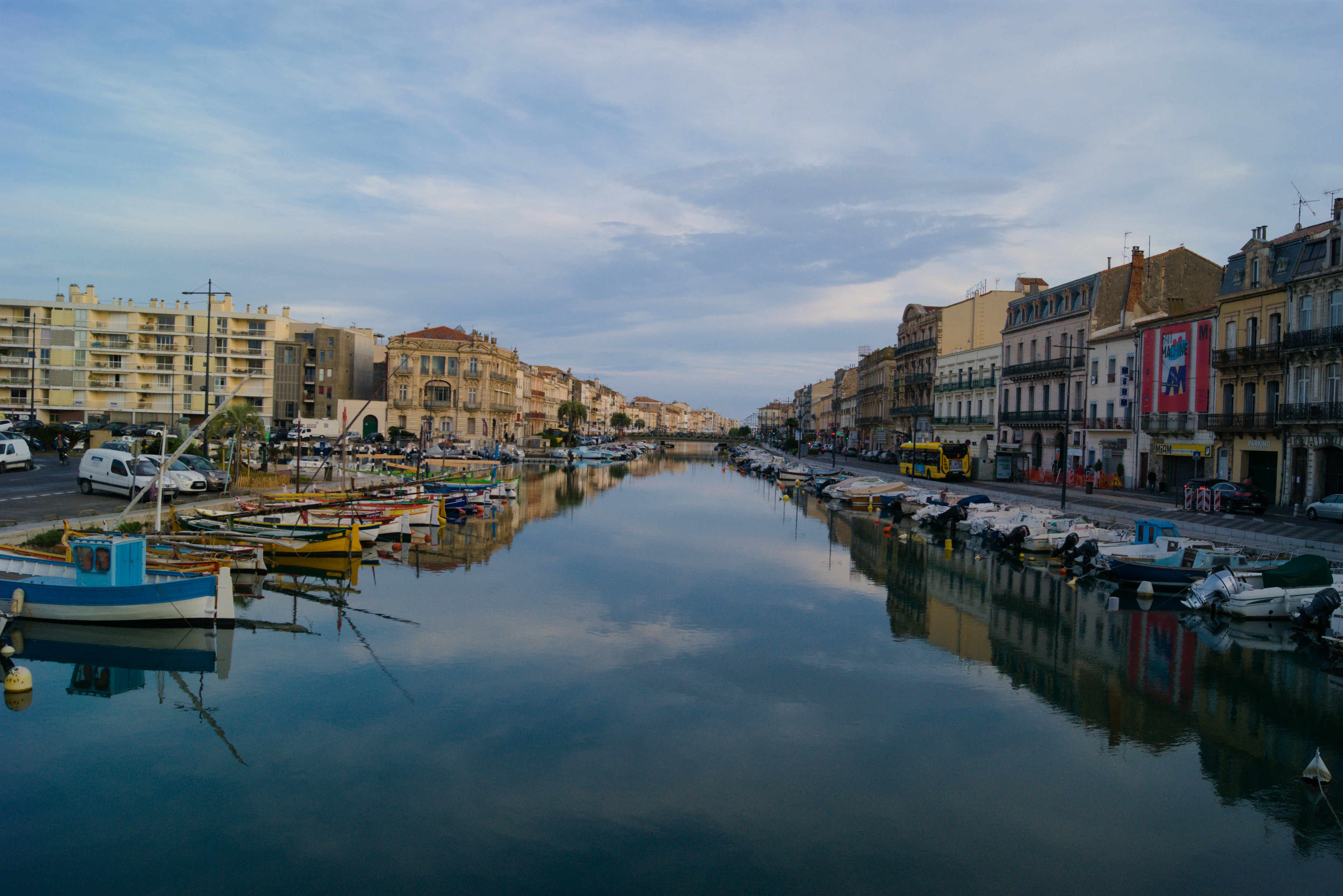 Calm canal waters reflecting historic buildings and moored boats under a soft spring sky.