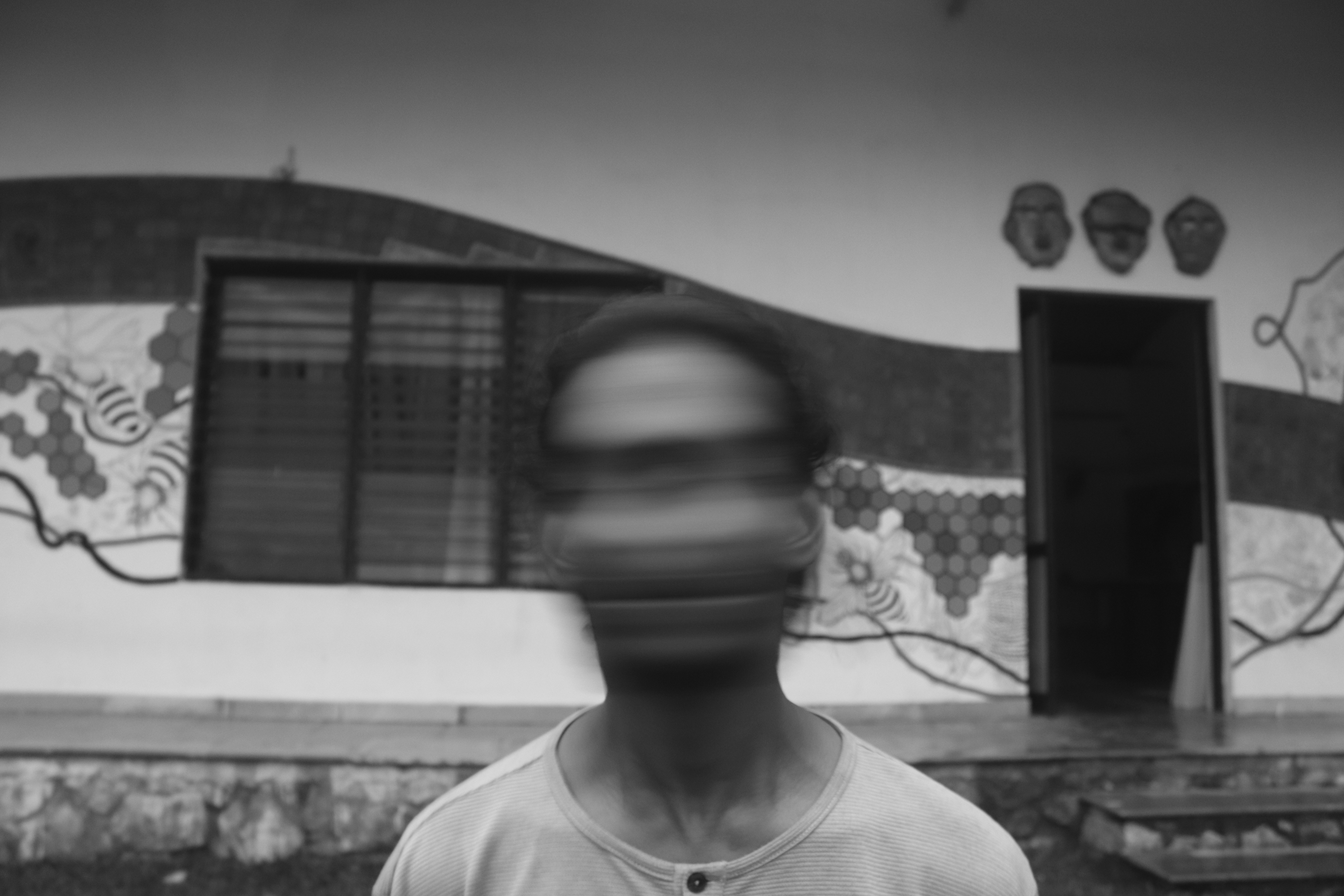 Blurred face of a person standing in front of a mural and an open door, creating a sense of motion.