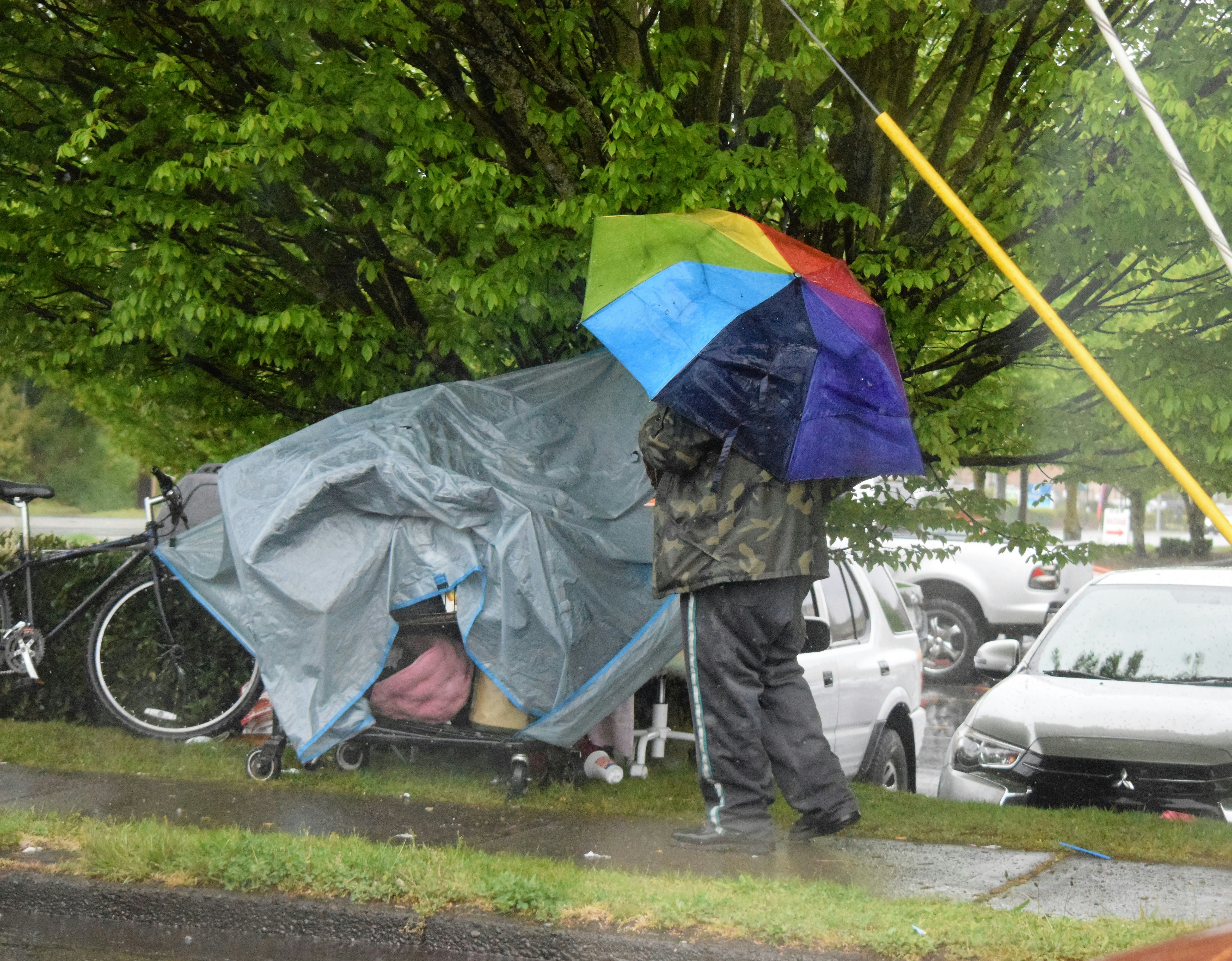 Rainbow Umbrella Guards a Makeshift Shelter on a Rainy City Street