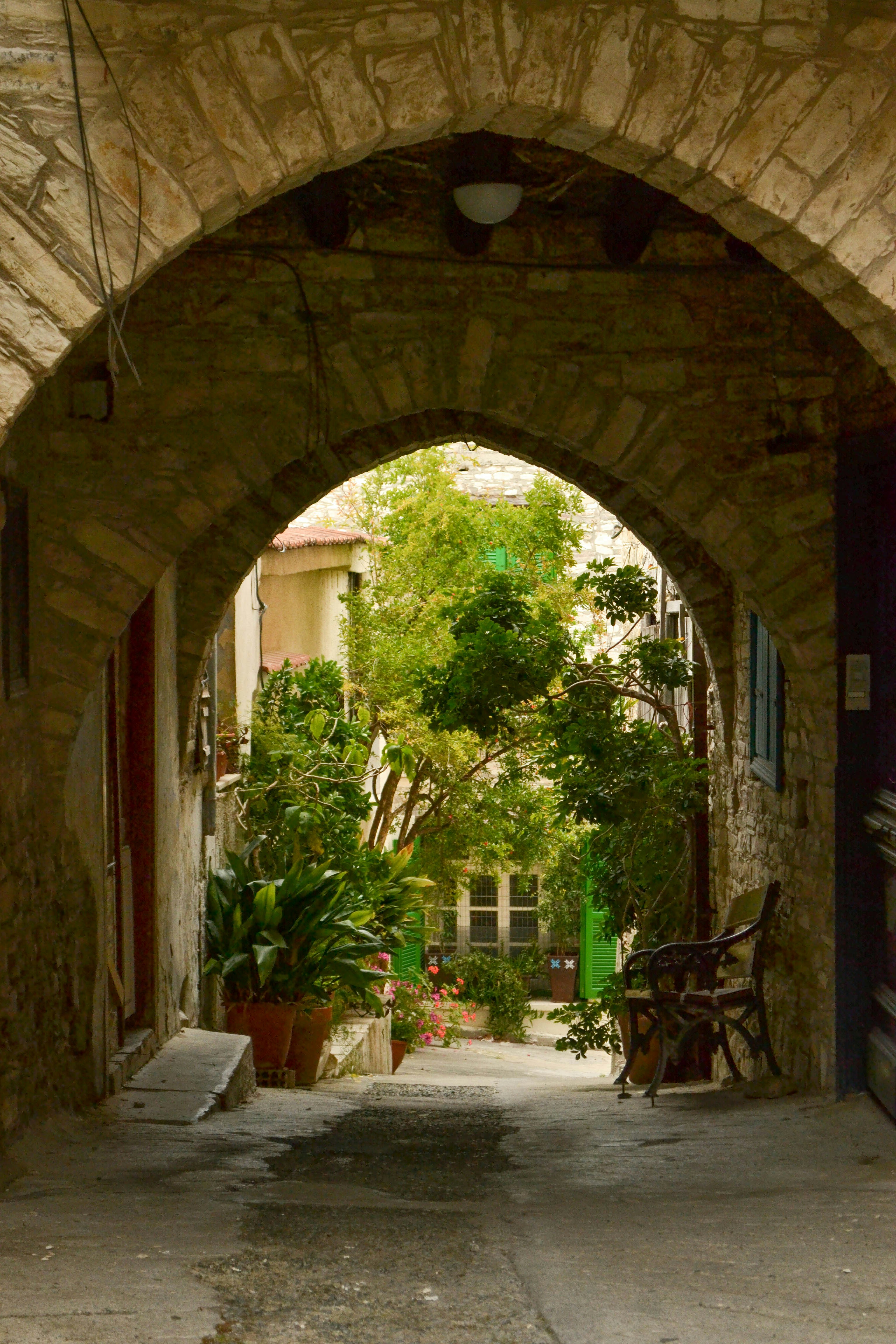 village Lefkara, Cyprus | a stone archway with a bench and potted plants