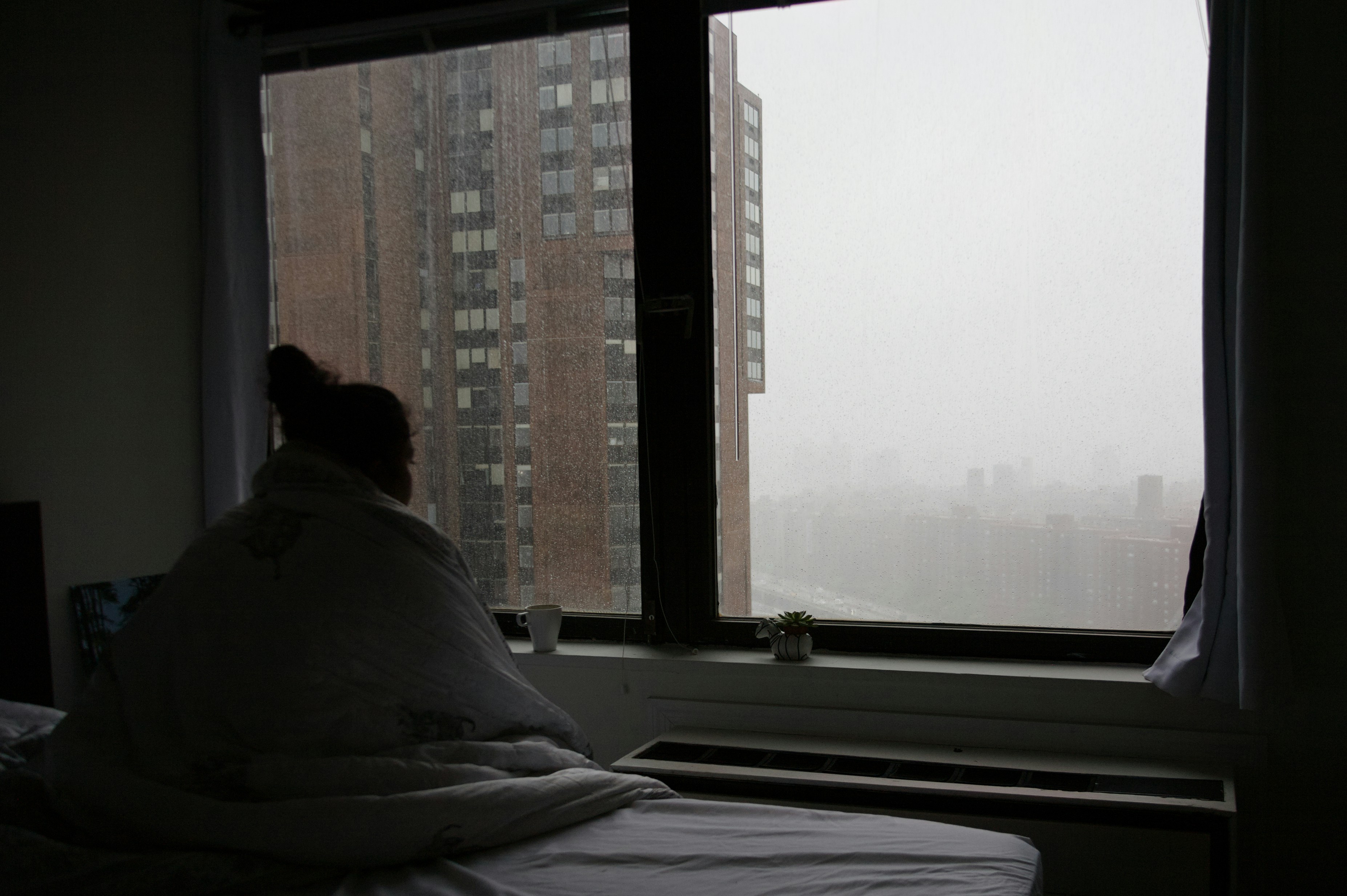 Person wrapped in a blanket gazing out a window at a foggy cityscape.