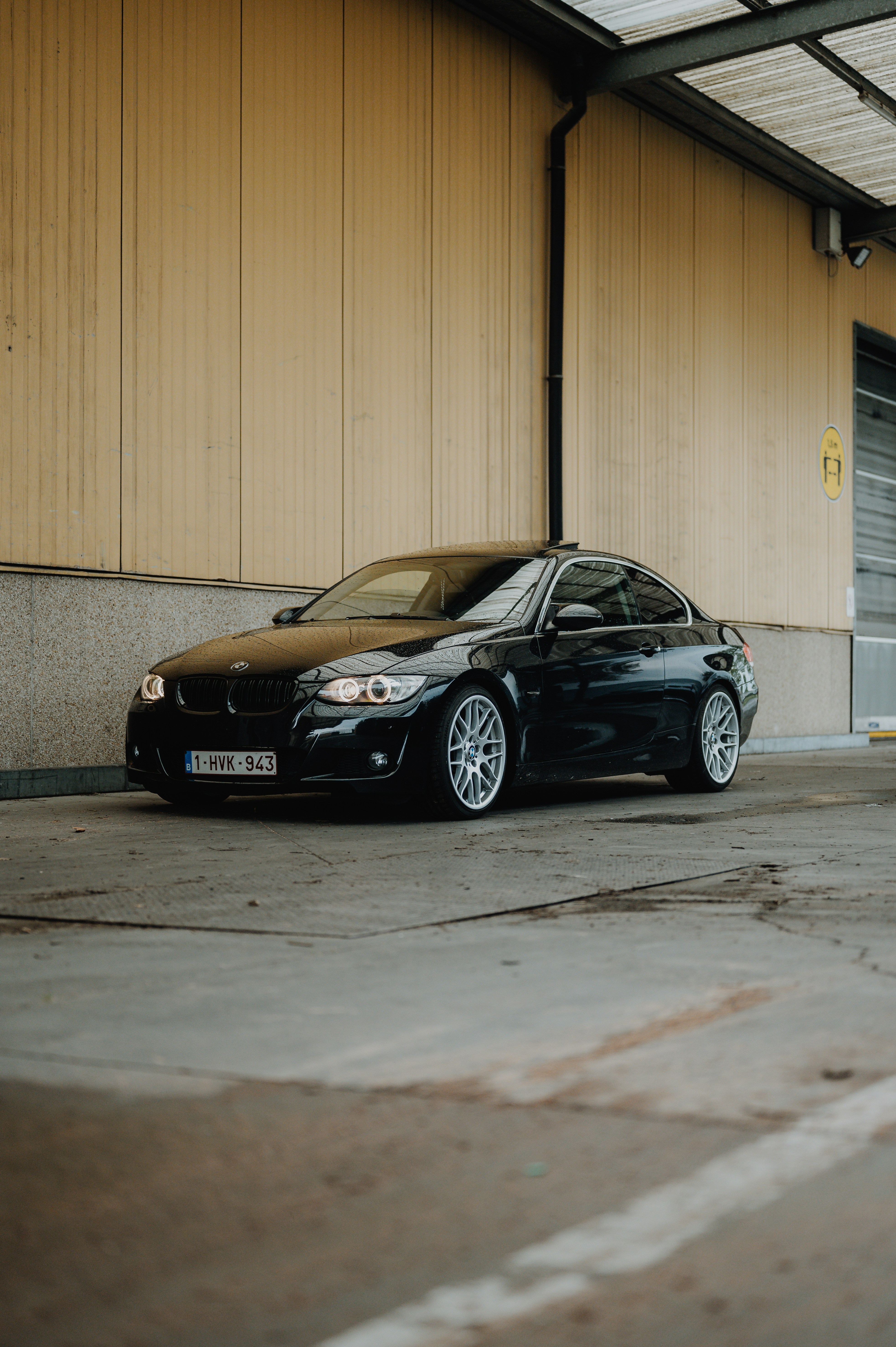 Sleek black BMW parked against a textured wall in an industrial setting, showcasing its modern design and elegance.