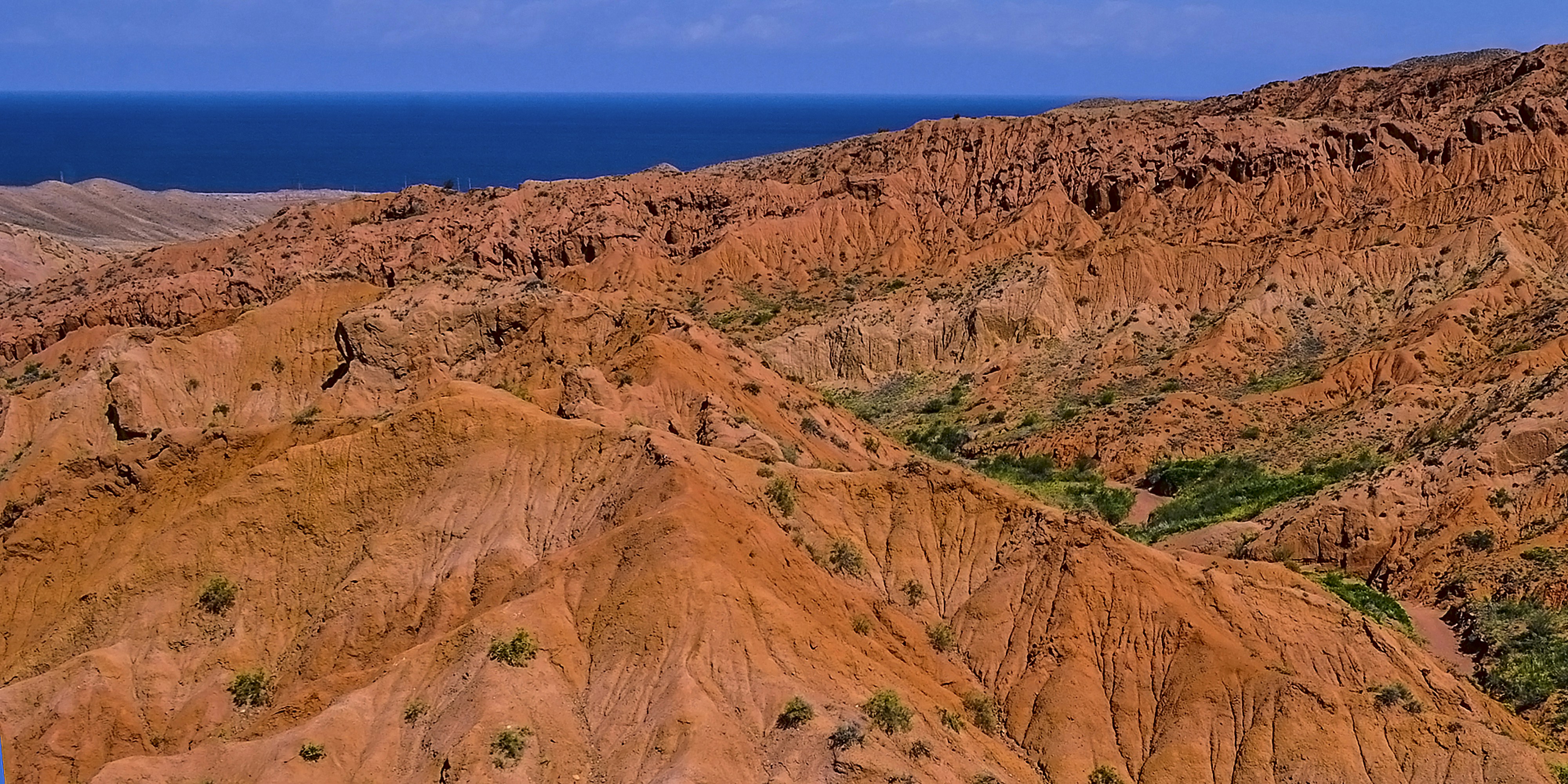 Wind-etched Red Badlands Meet the Distant Sea Horizon