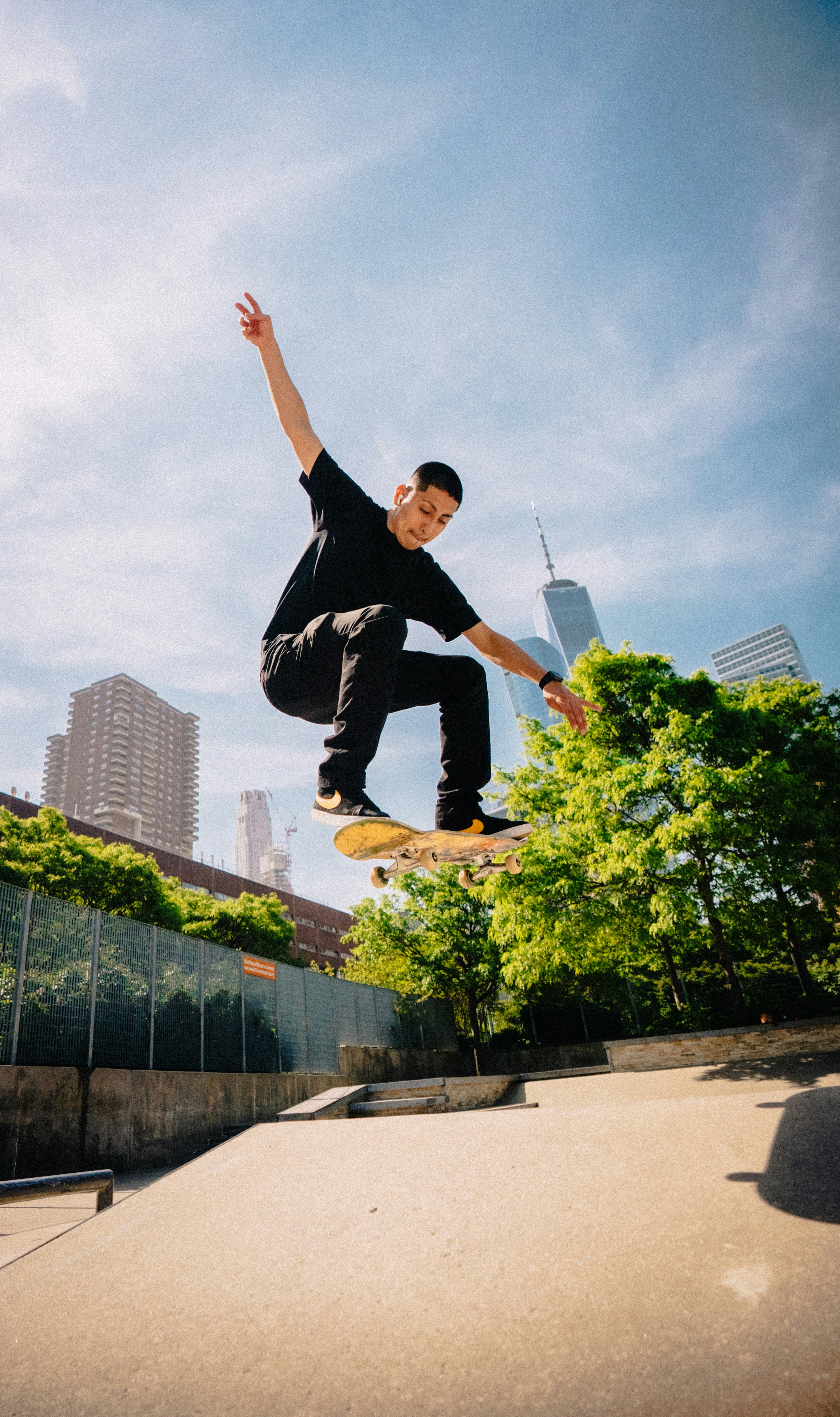 Skateboarder performing an impressive jump in a city park, surrounded by greenery and urban architecture.