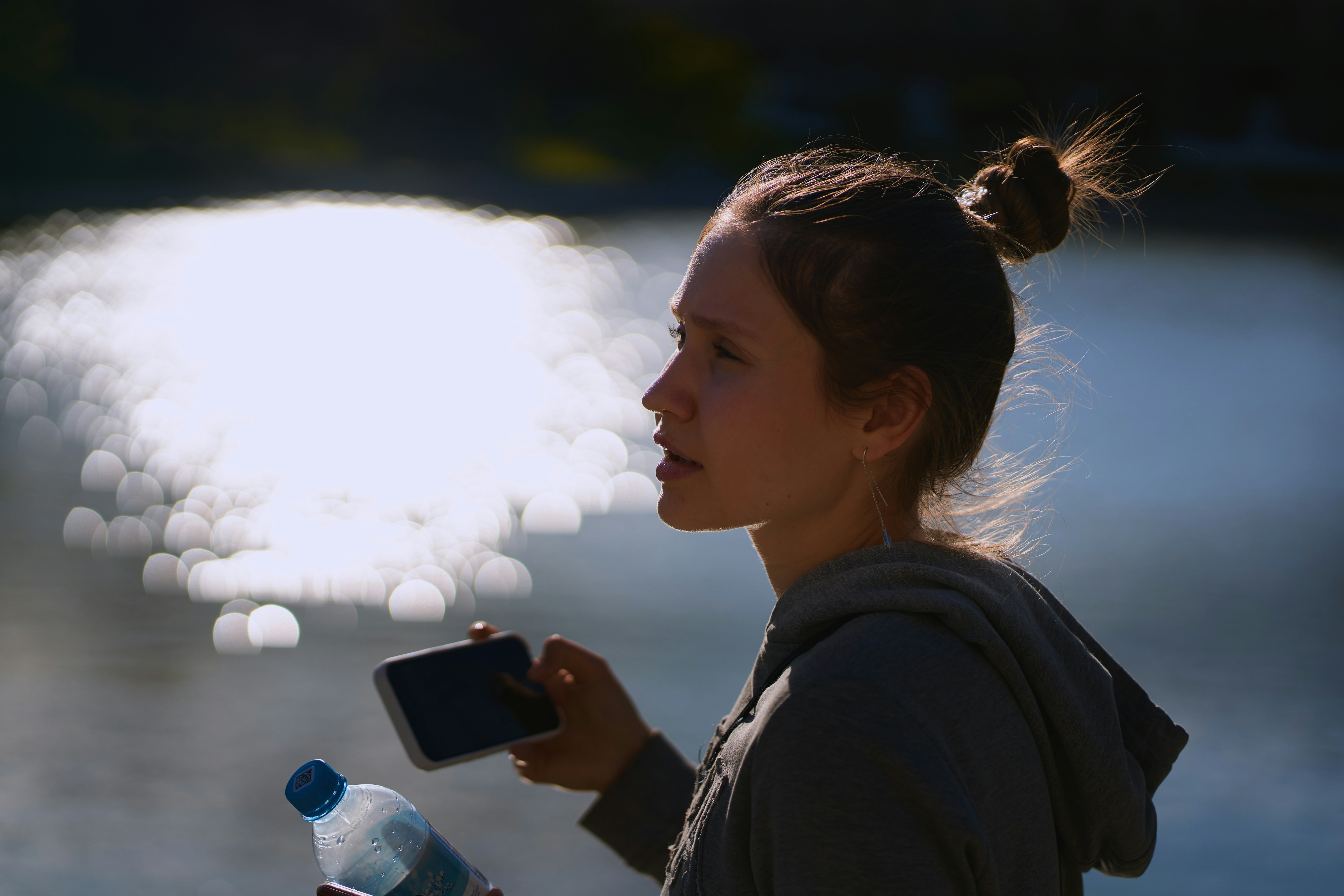 Backlit Profile by the River: A Quiet Moment with a Phone and Water Bottle