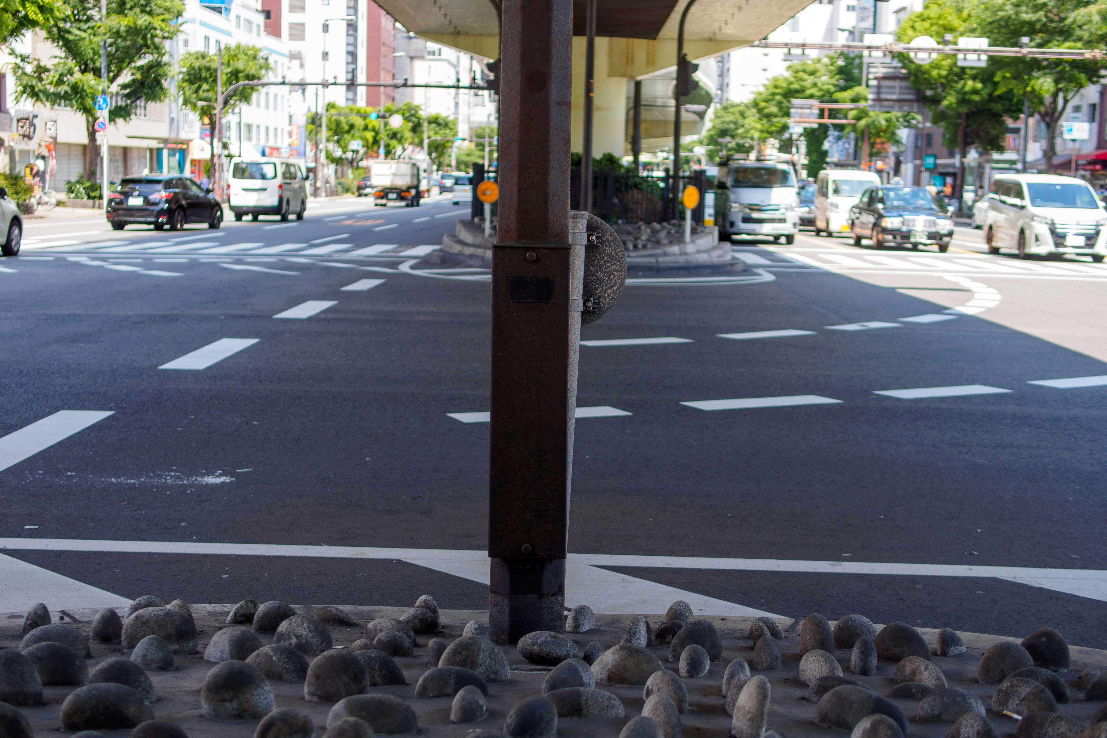 Vertical Anchor Under the City Canopy: Pebbles in the Foreground, Traffic in Motion