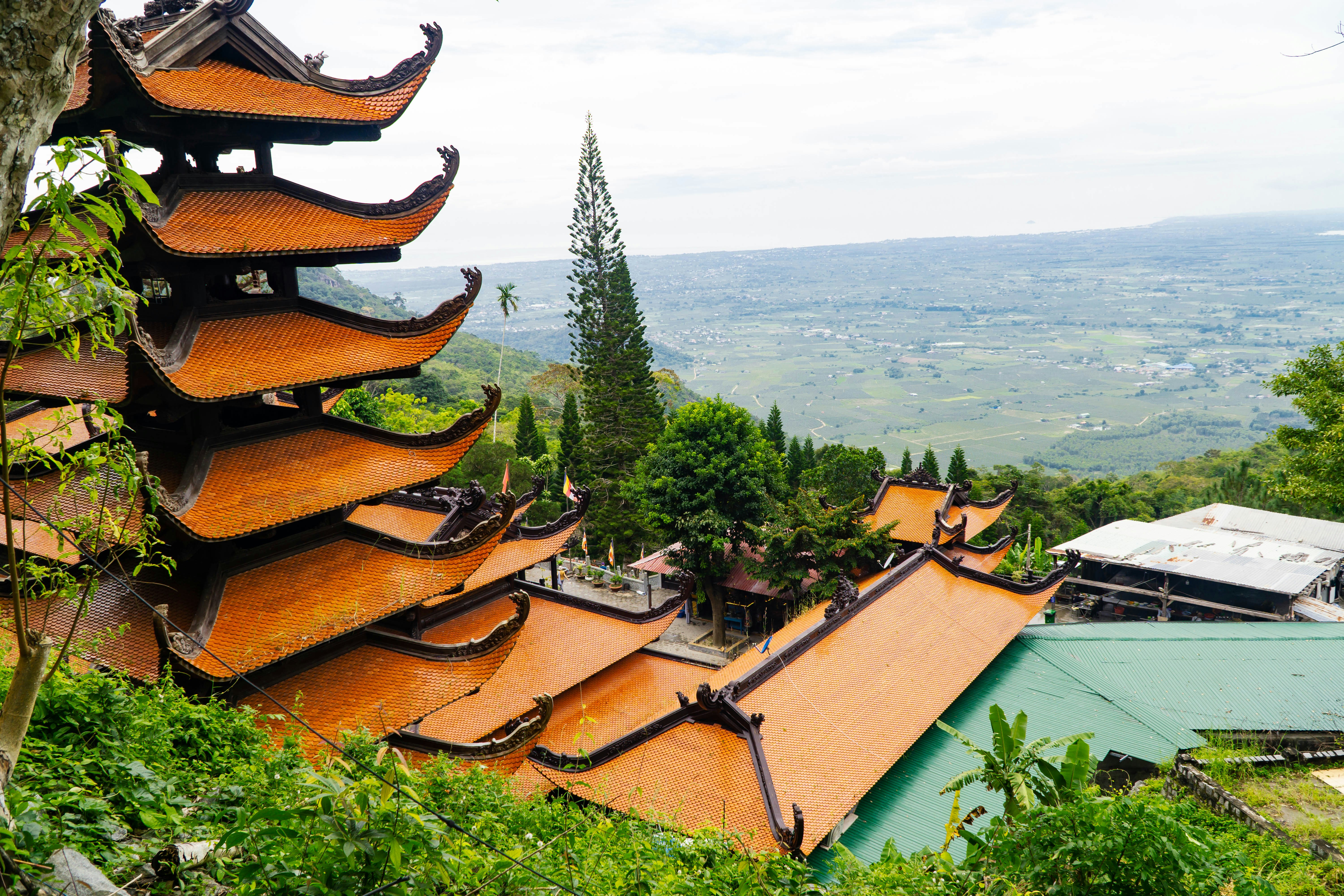 Traditional pagoda structure nestled in lush greenery, overlooking a vast valley. The intricate architecture harmonizes with the surrounding landscape.