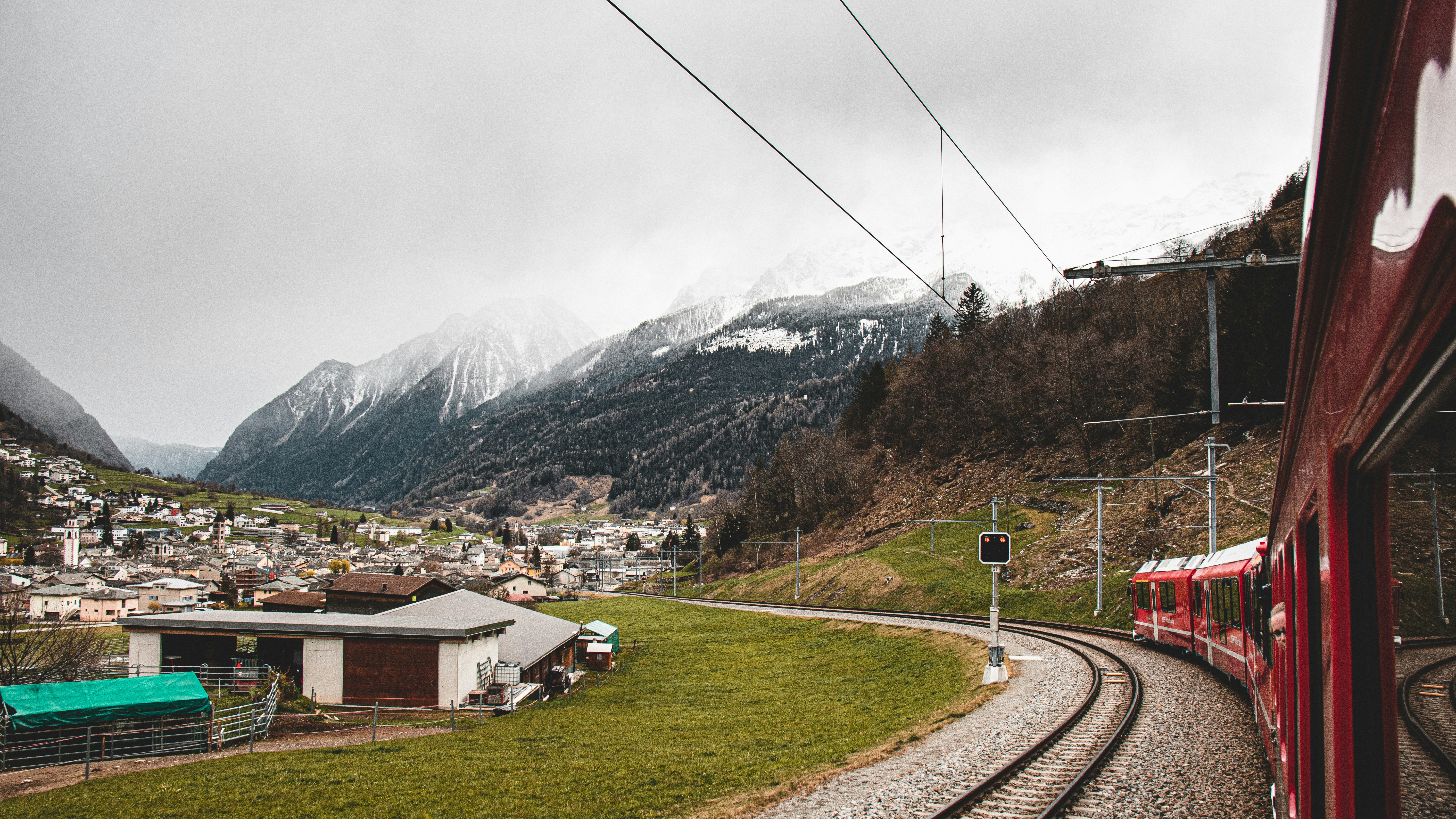 a red train traveling down train tracks next to a lush green hillside