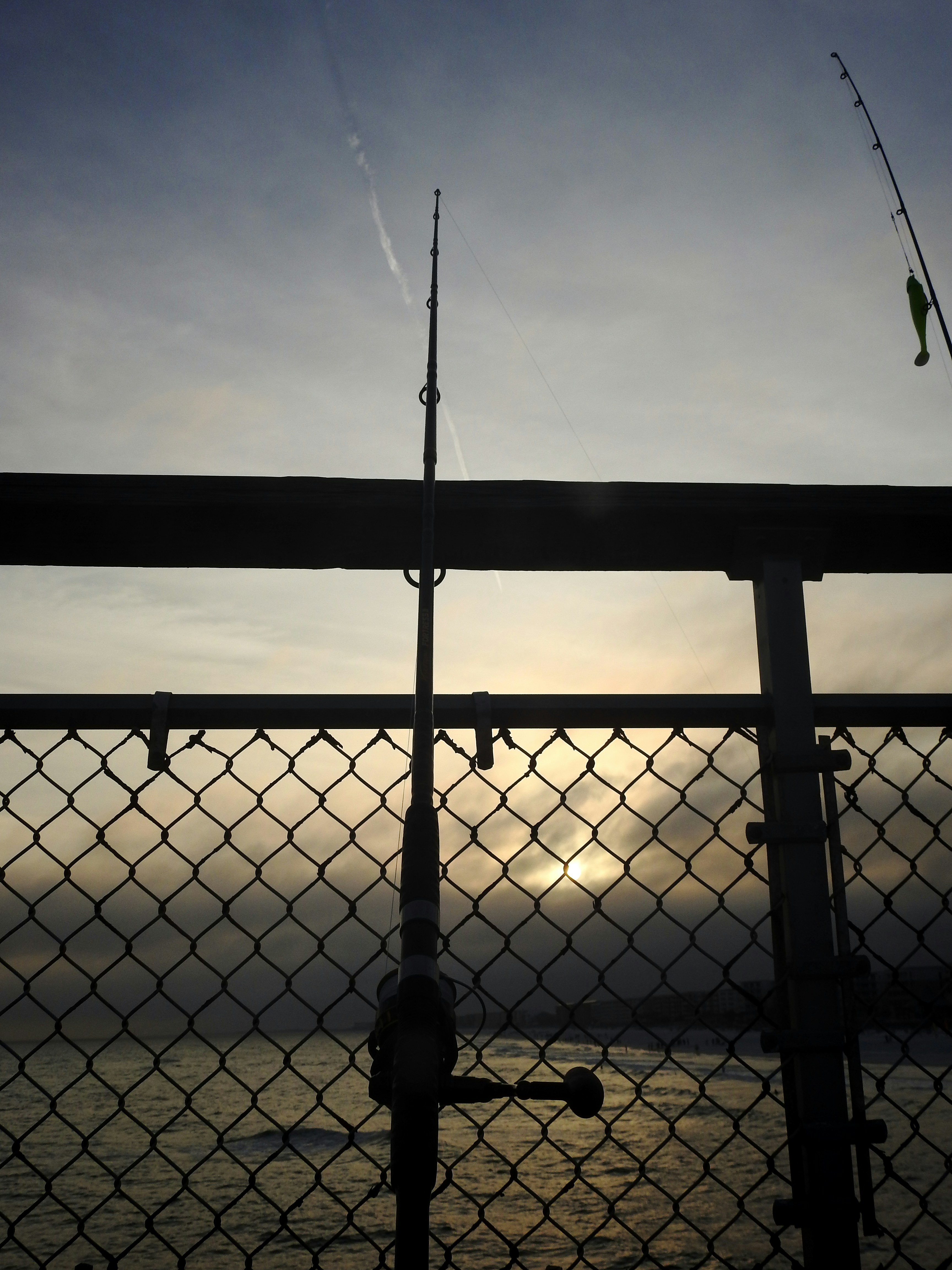 Rimmed by Chain-Link Silence: A Dockside Fishing Rod at Dusk