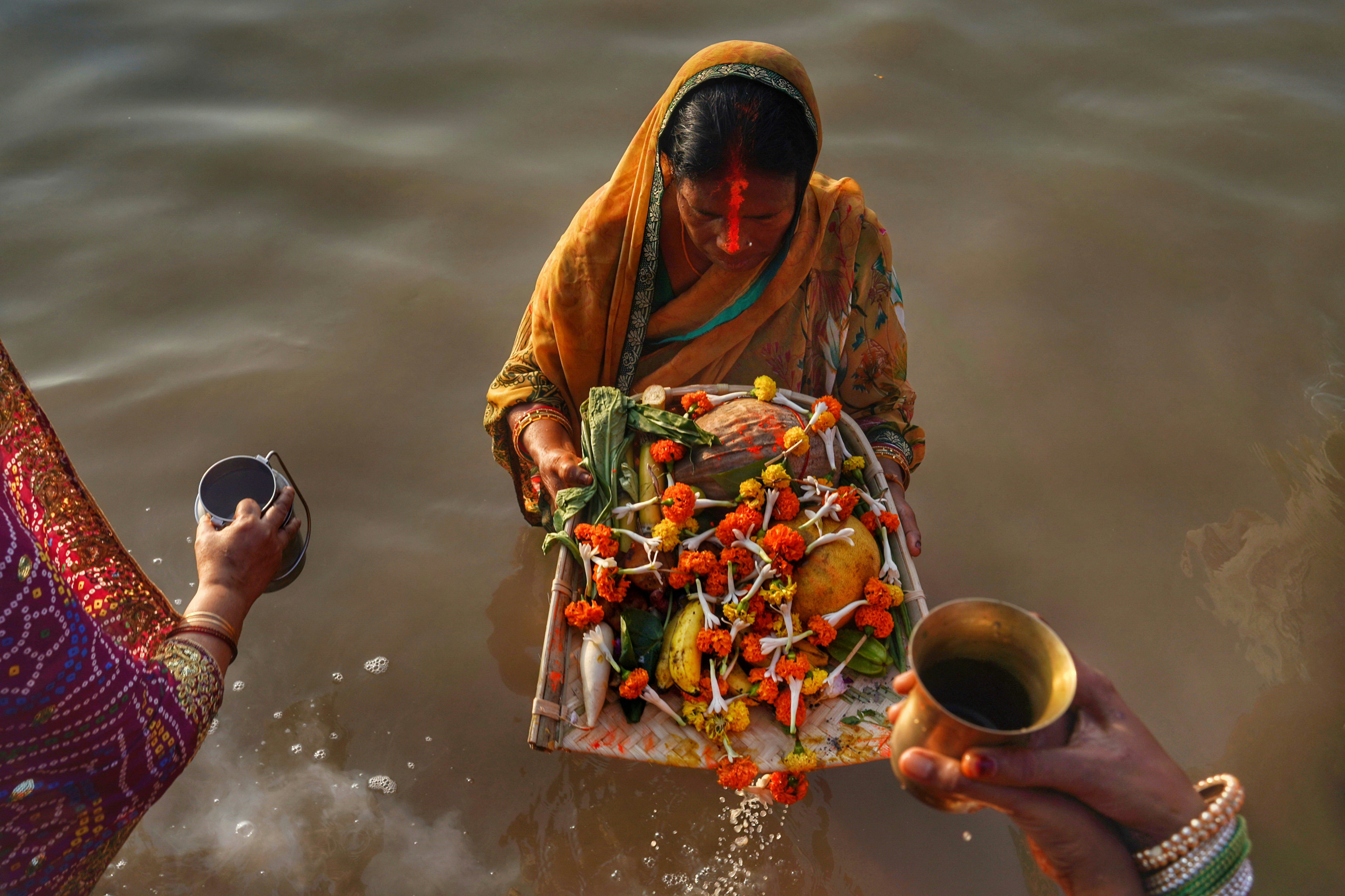 Woman in traditional attire holds a basket of flowers and fruits in water.