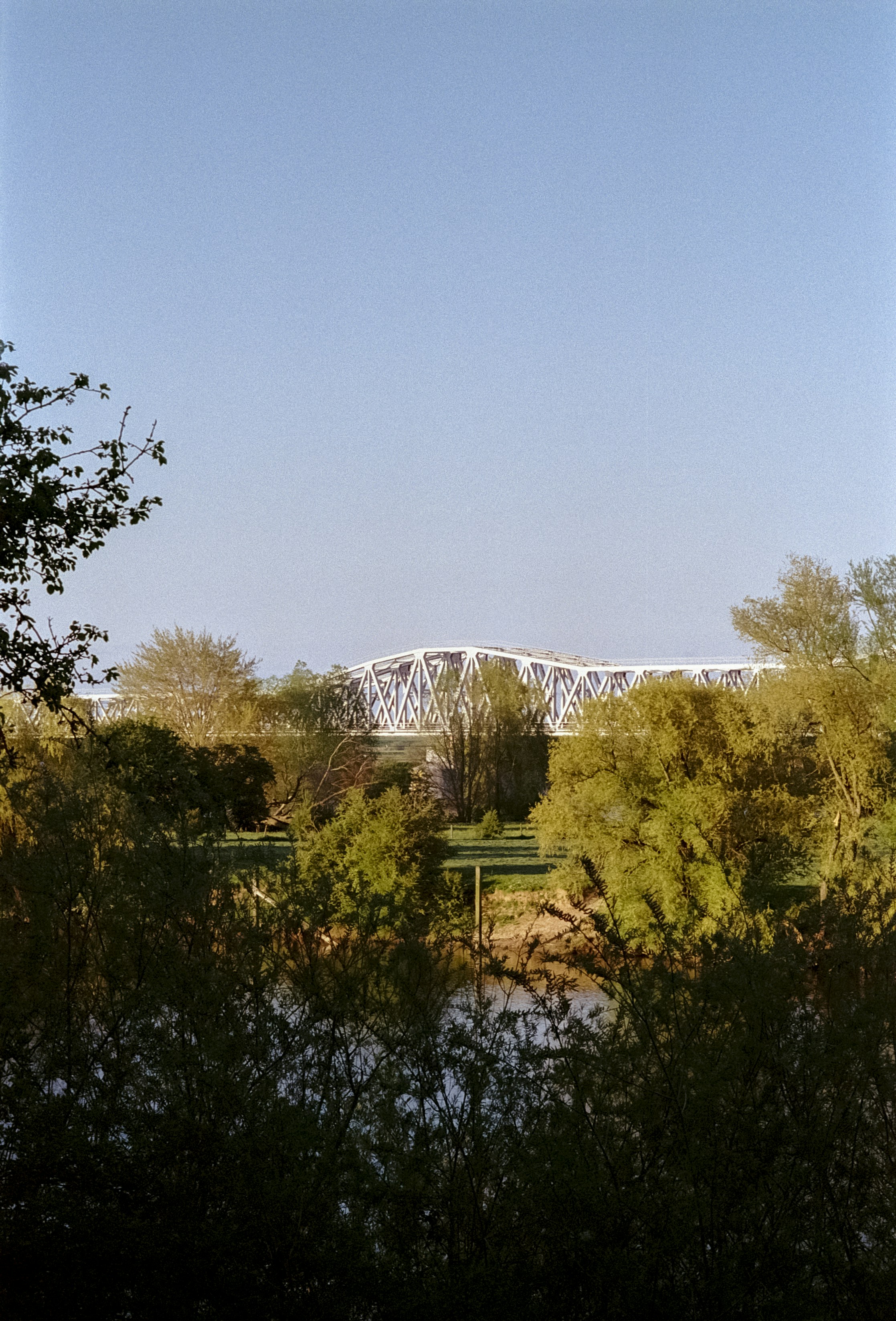 Blue Sky over a White Truss Bridge Framing a Quiet River