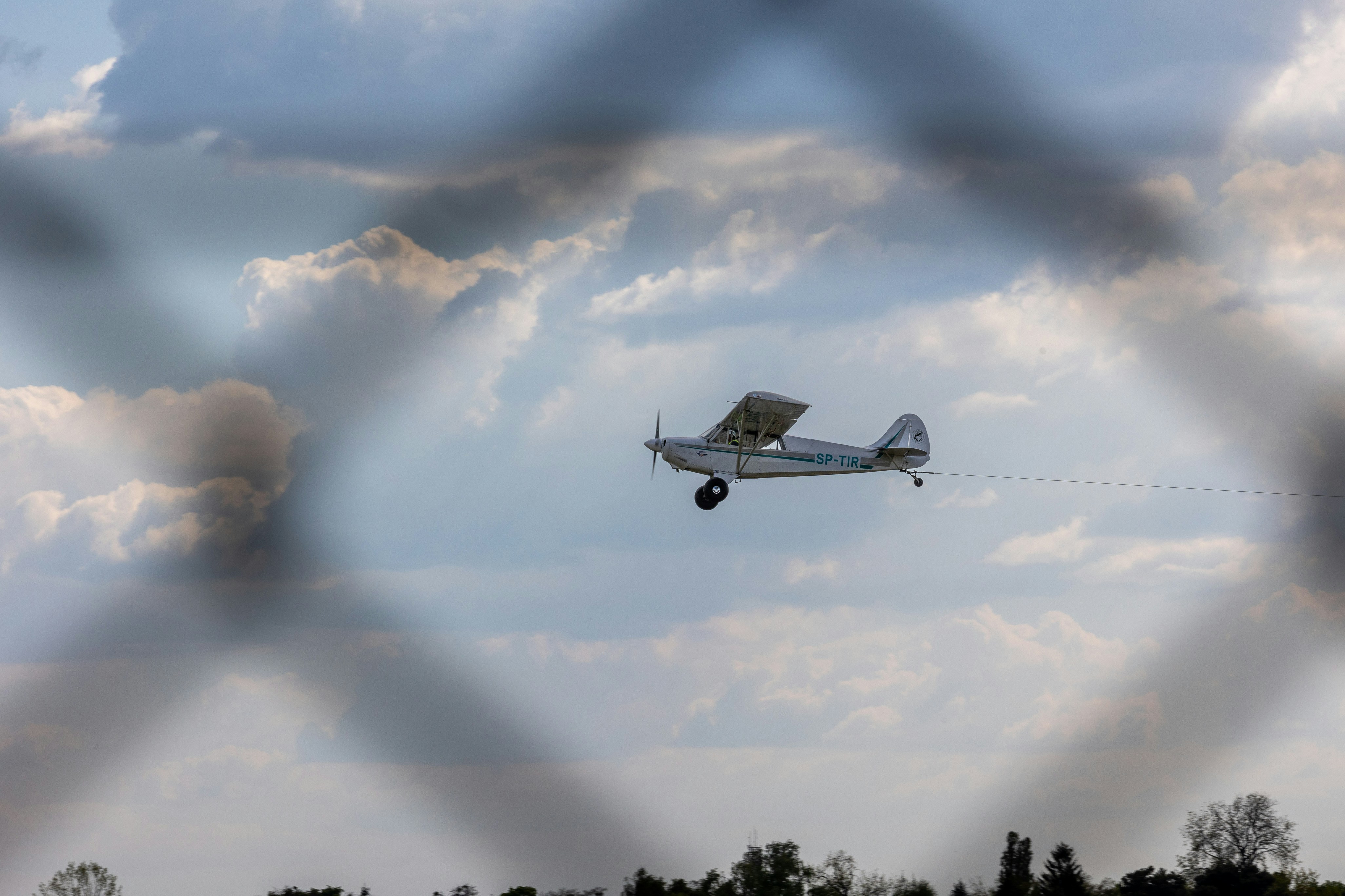 Lone Plane Crossing a Cloudy Expanse, Framed by Faint Fence