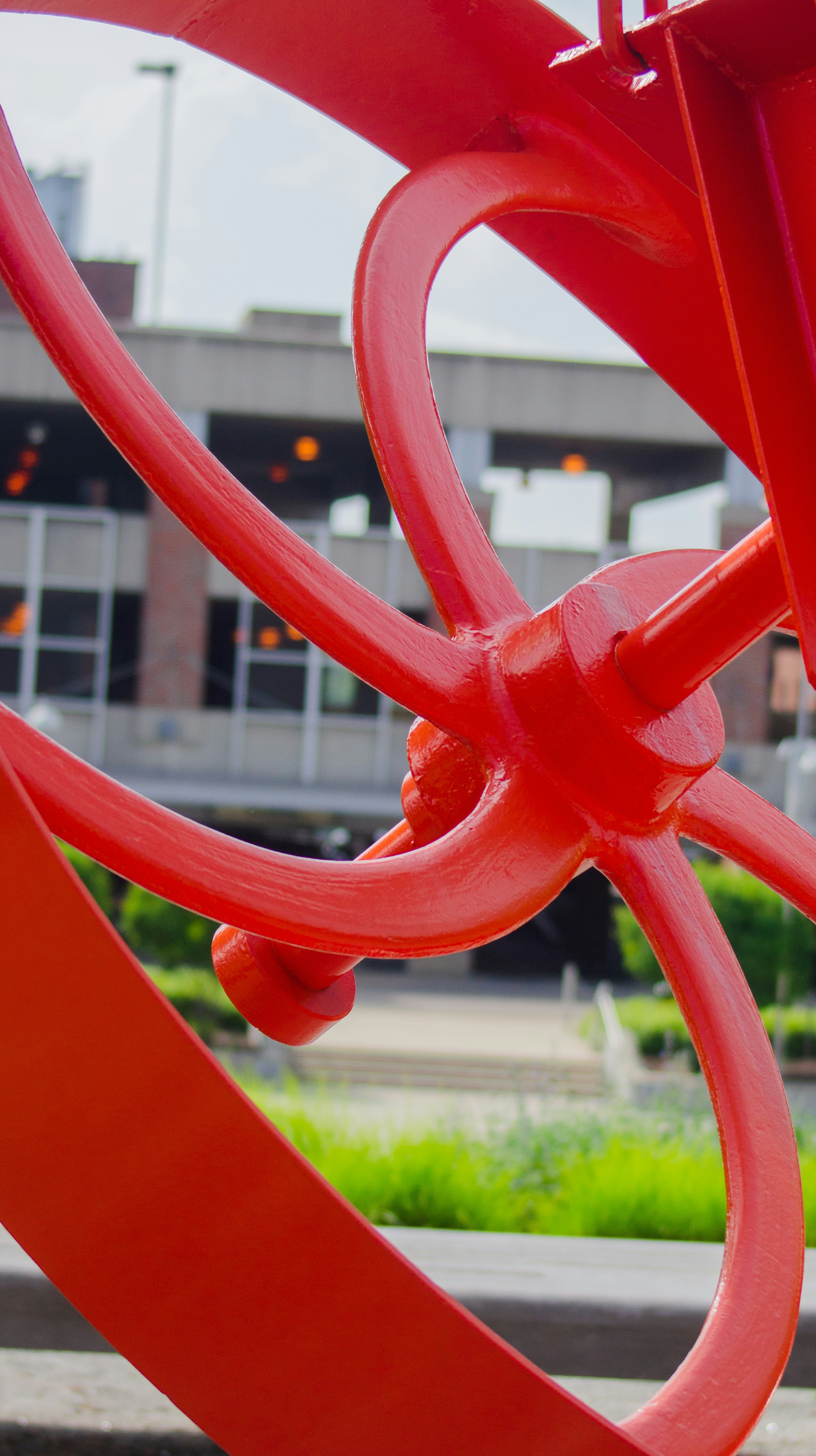 Abstract red metal sculpture with circular elements set against an urban backdrop.