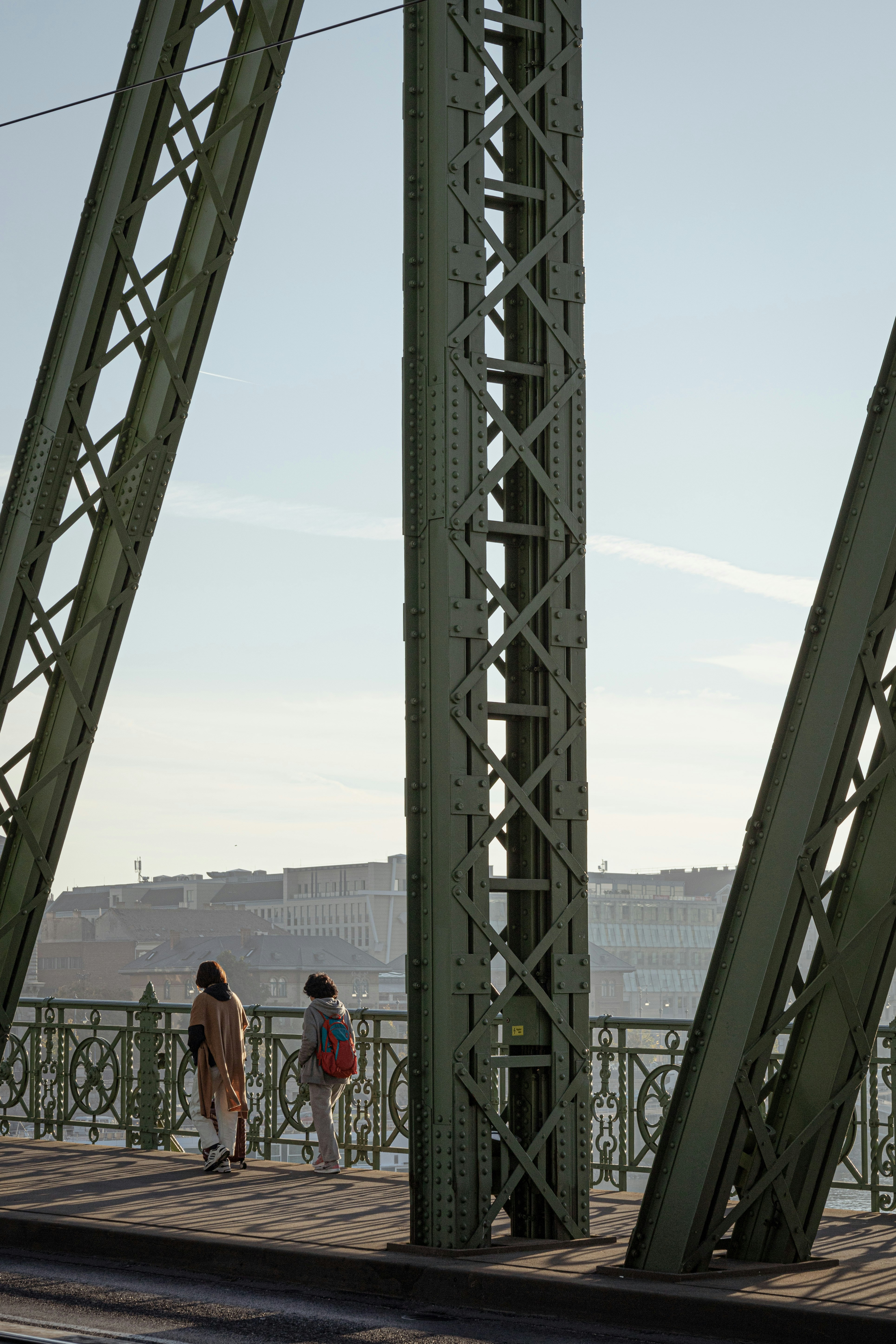Between Trusses: Two Travelers on a Verdigris Bridge Over the River