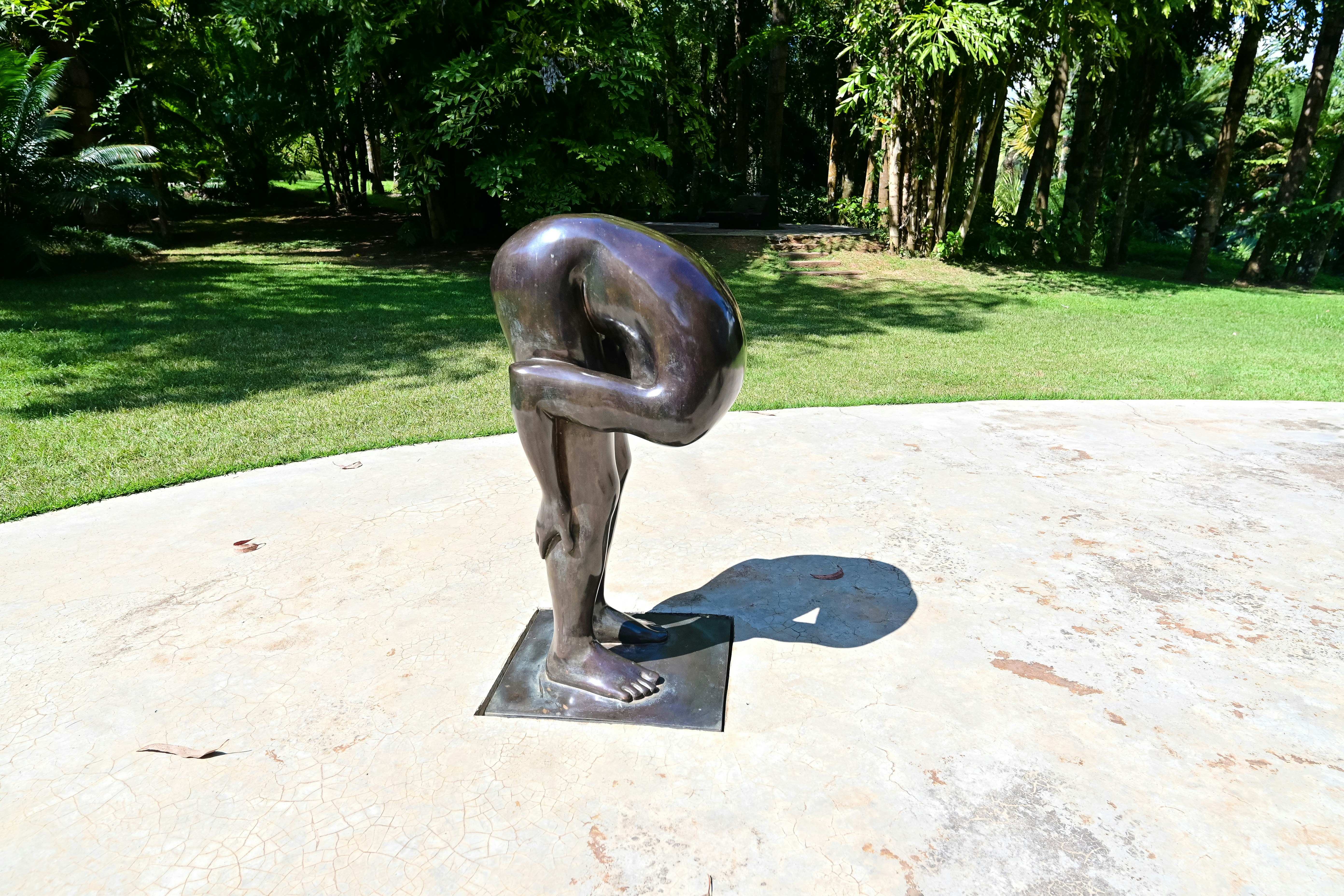 Contemplative Bend: Bronze Figure on a Sunlit Park Platform