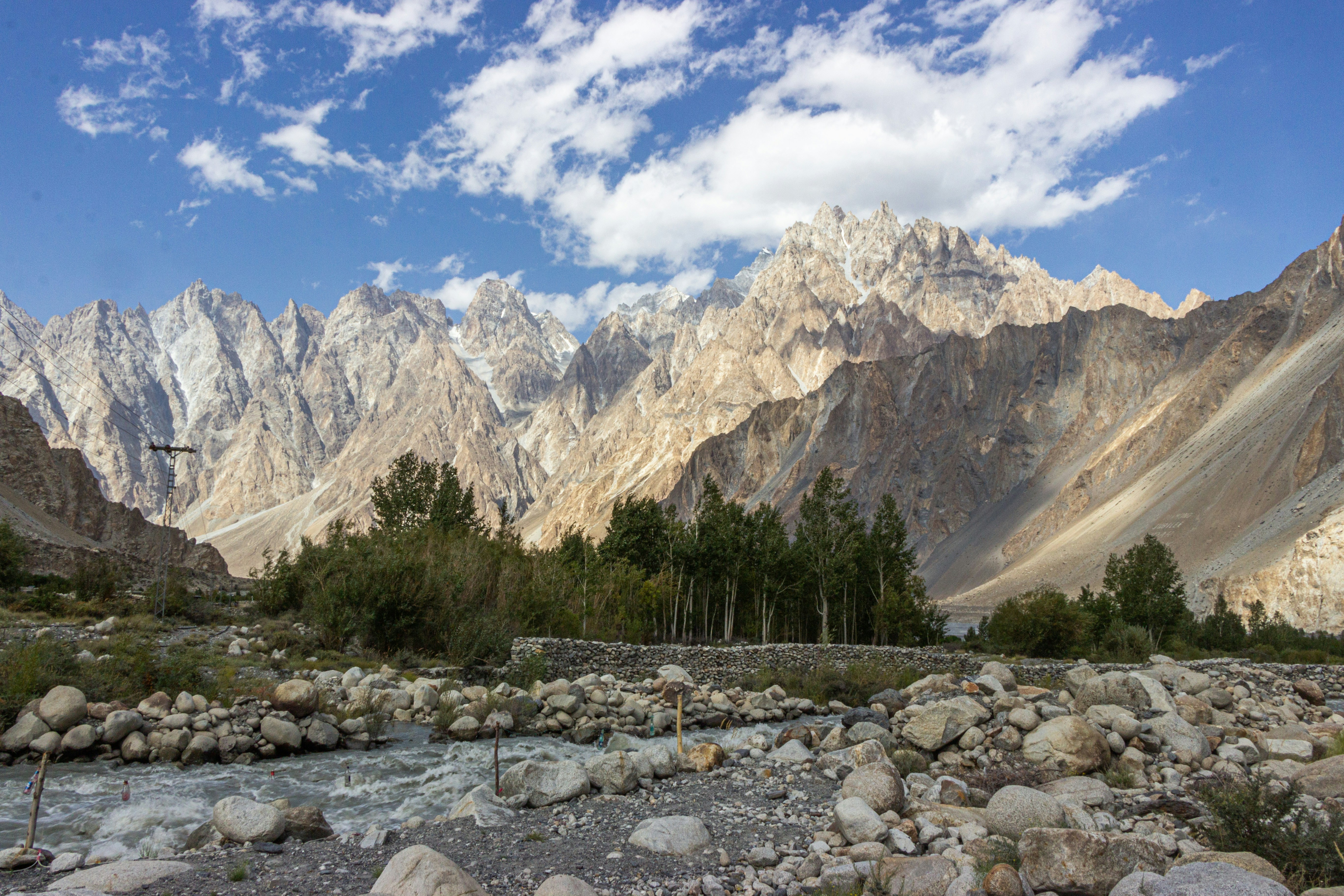 River winding through a rocky valley with towering mountains under a sky dotted with clouds.