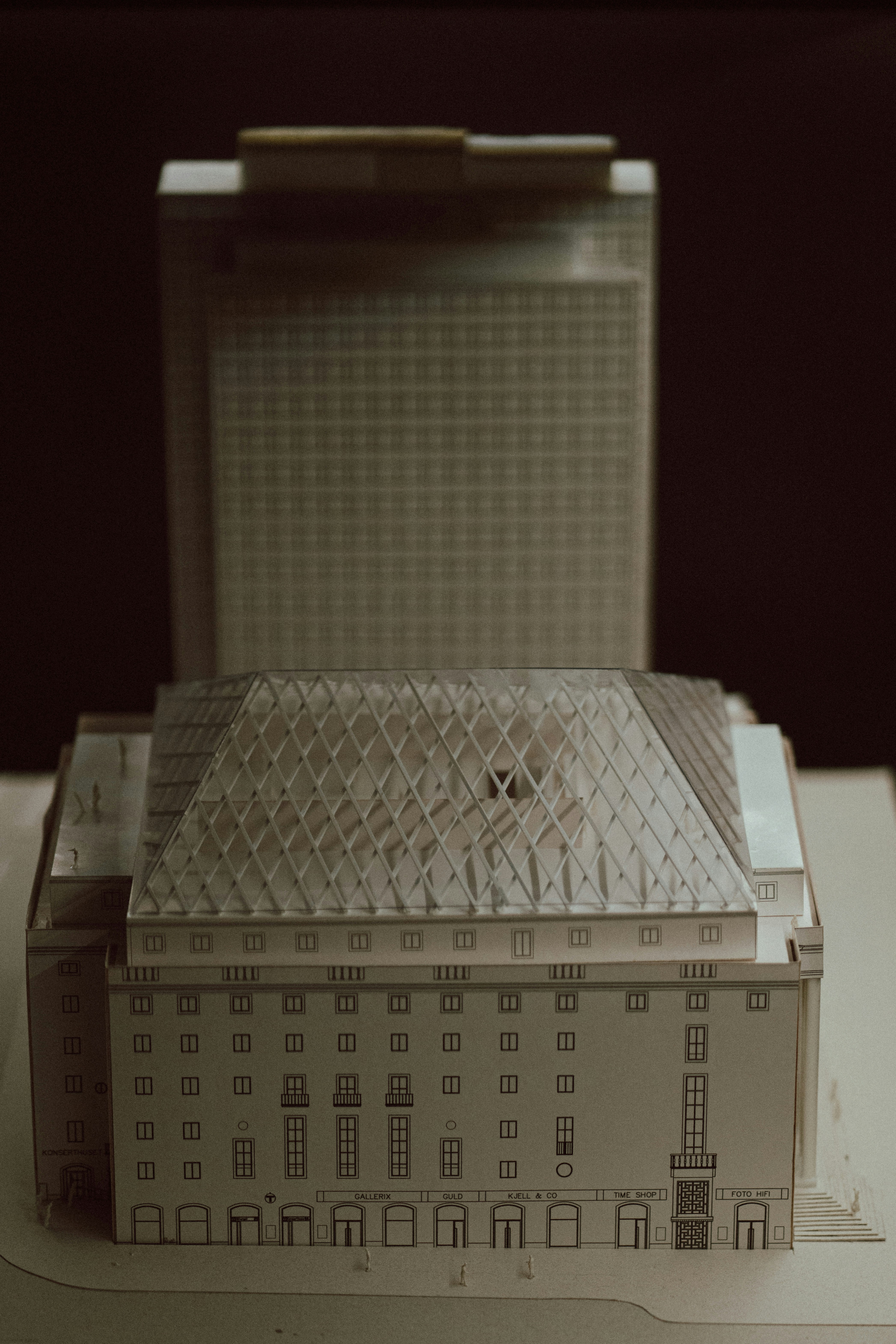 Detailed architectural model showcasing a building with a glass roof and intricate facade, set against a contrasting backdrop of a modern skyscraper.