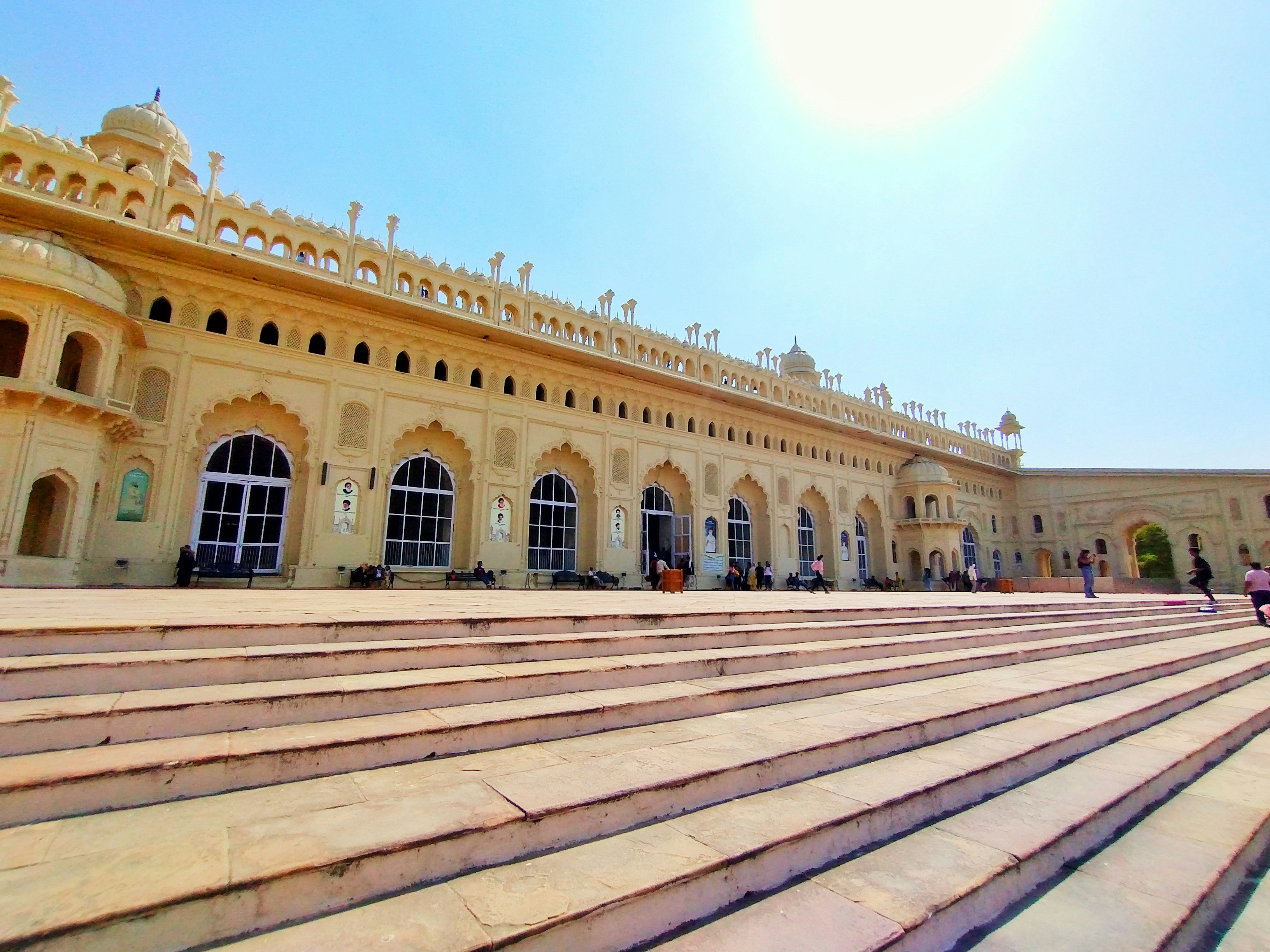 Photograph of a sunlit arched palace façade and broad stone steps leading to the entrance. The scene emphasizes architectural detail and open sky.