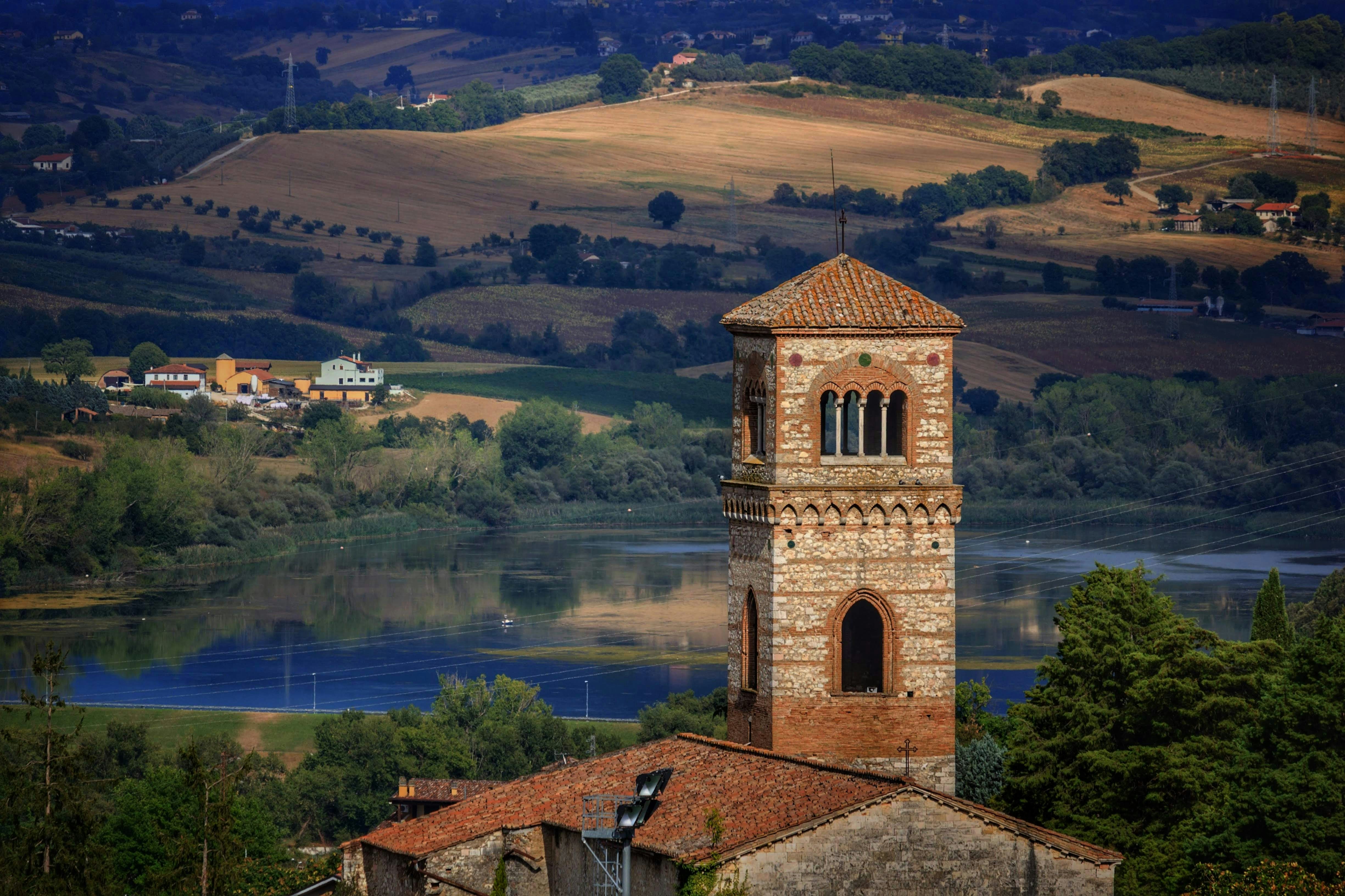 Historic church tower overlooking a serene lake amid rolling countryside.