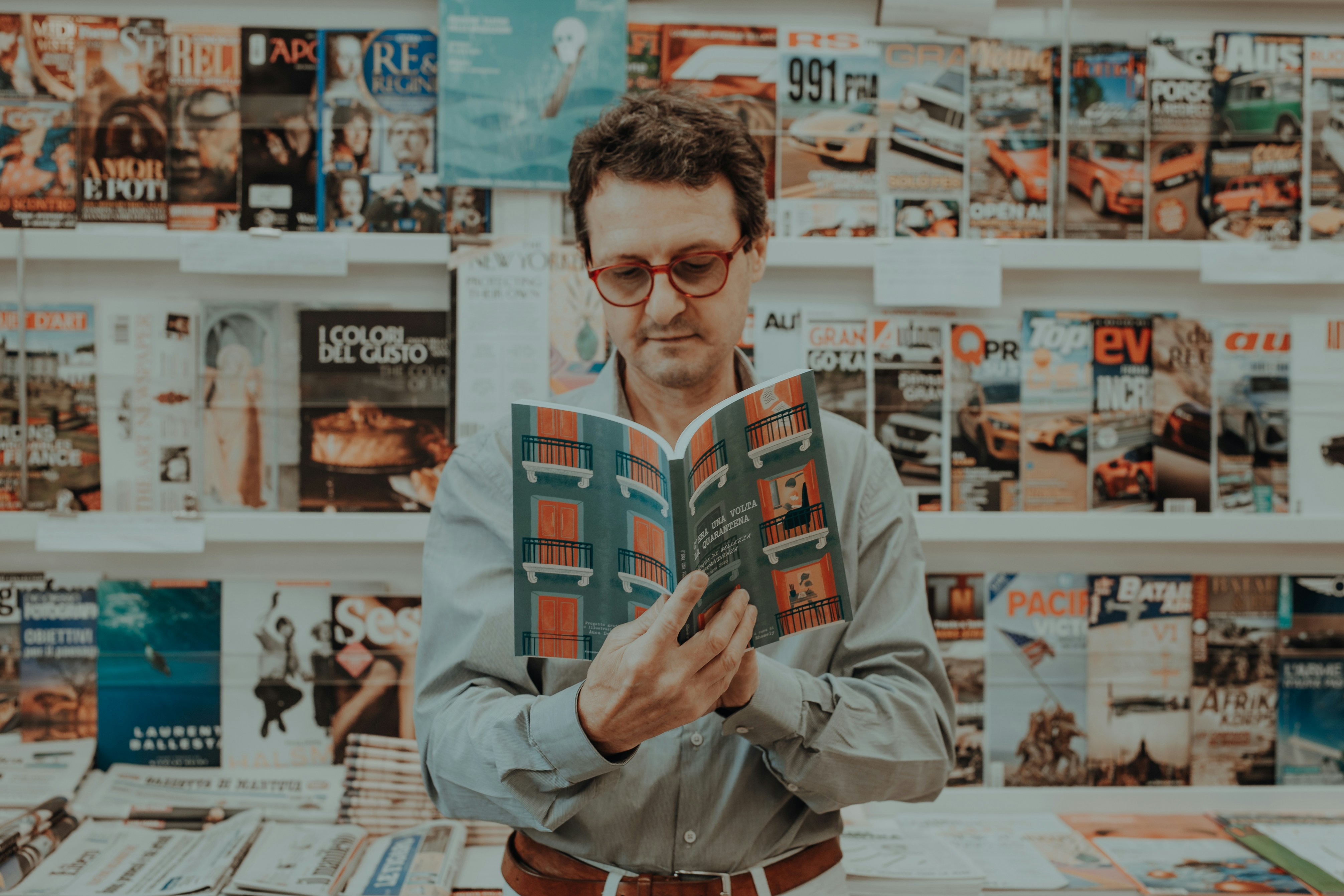A man reading a book in front of a wall of magazines photo – Free Book ...