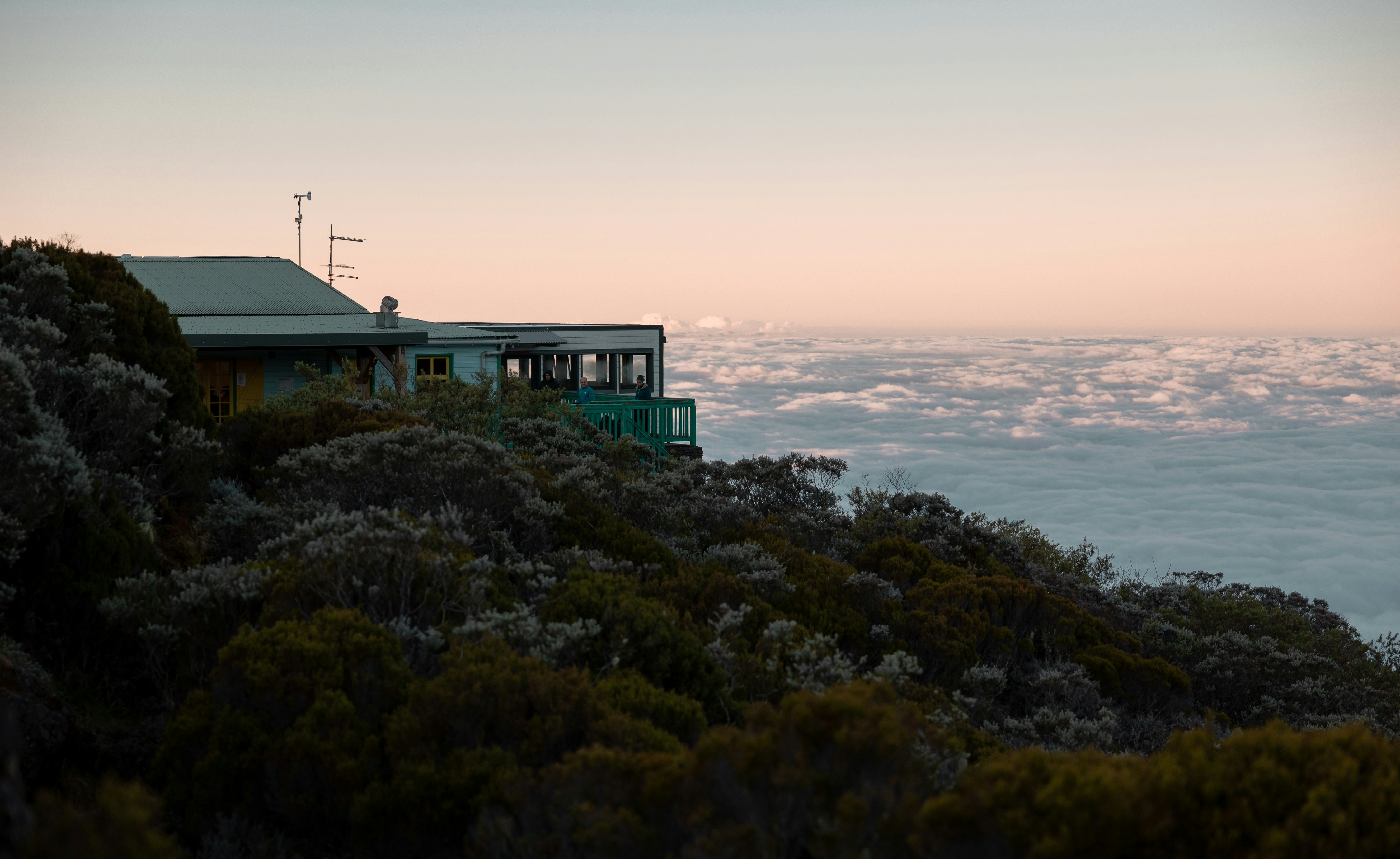 Coastal house perched on a rocky hill with ocean waves under a twilight sky.