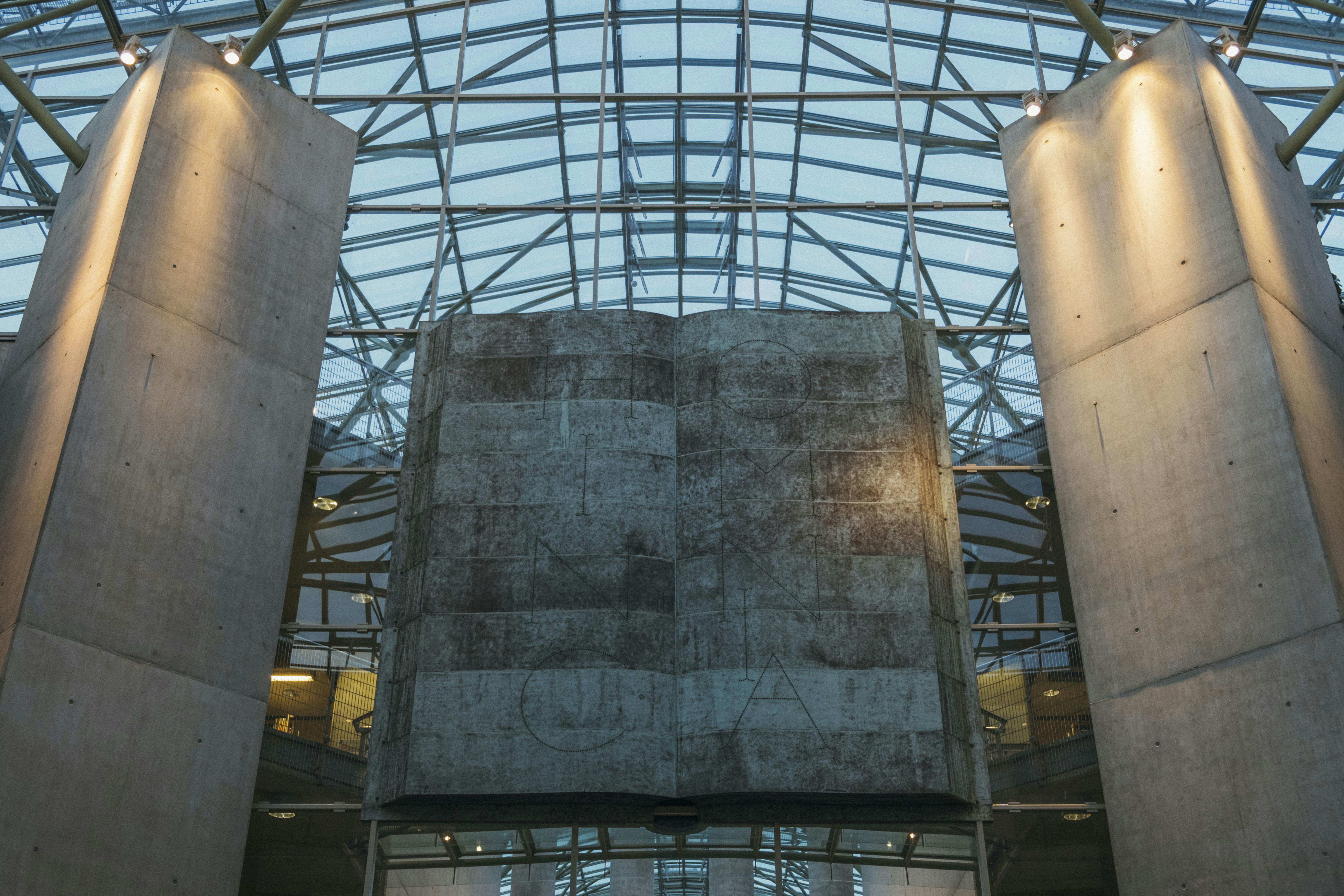Symmetry Beneath the Glass Roof: A Monumental Concrete Facade Framed by Steel