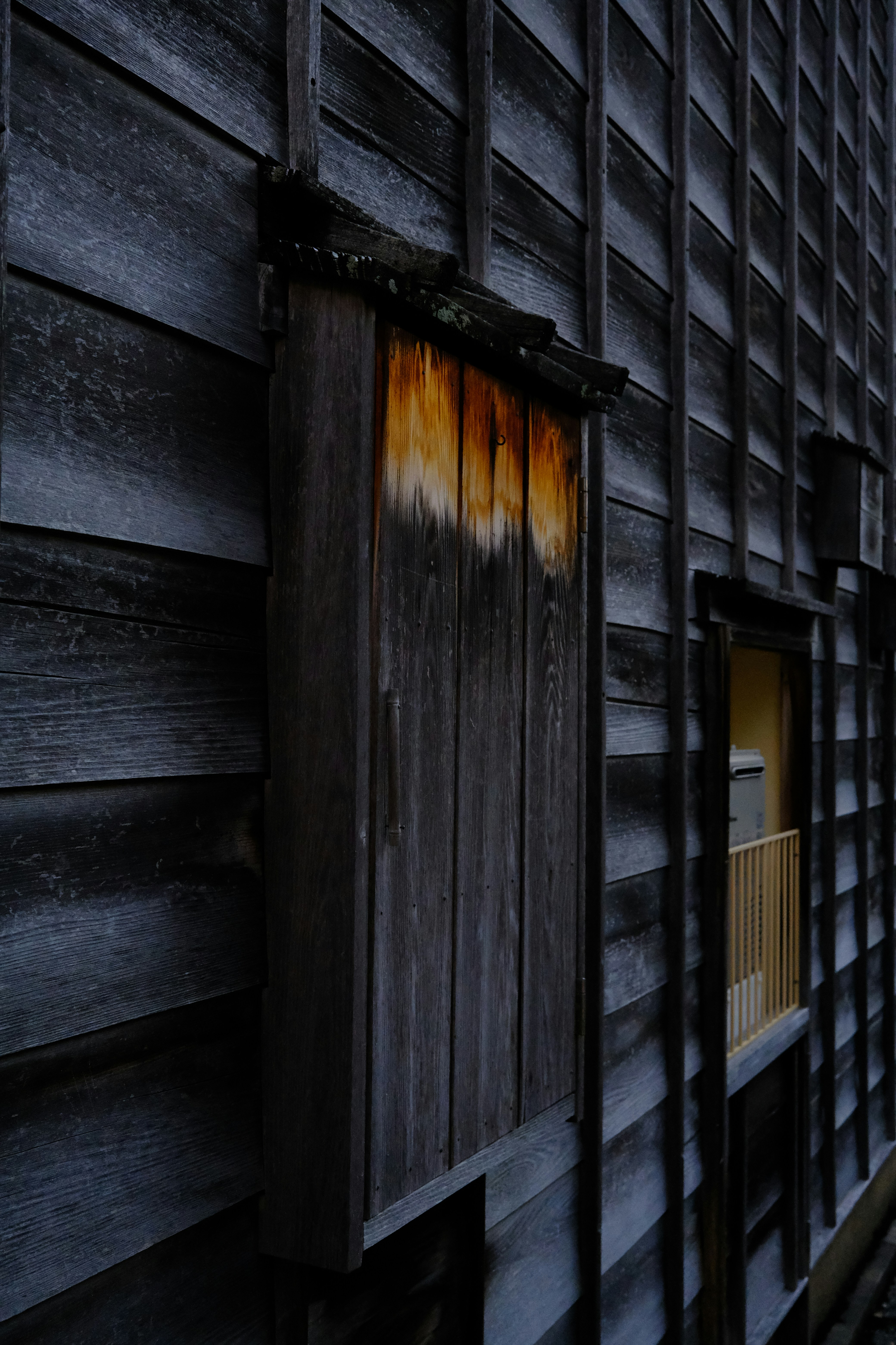 Ember on the Weathered Facade: A Doorway Among Dark Timber