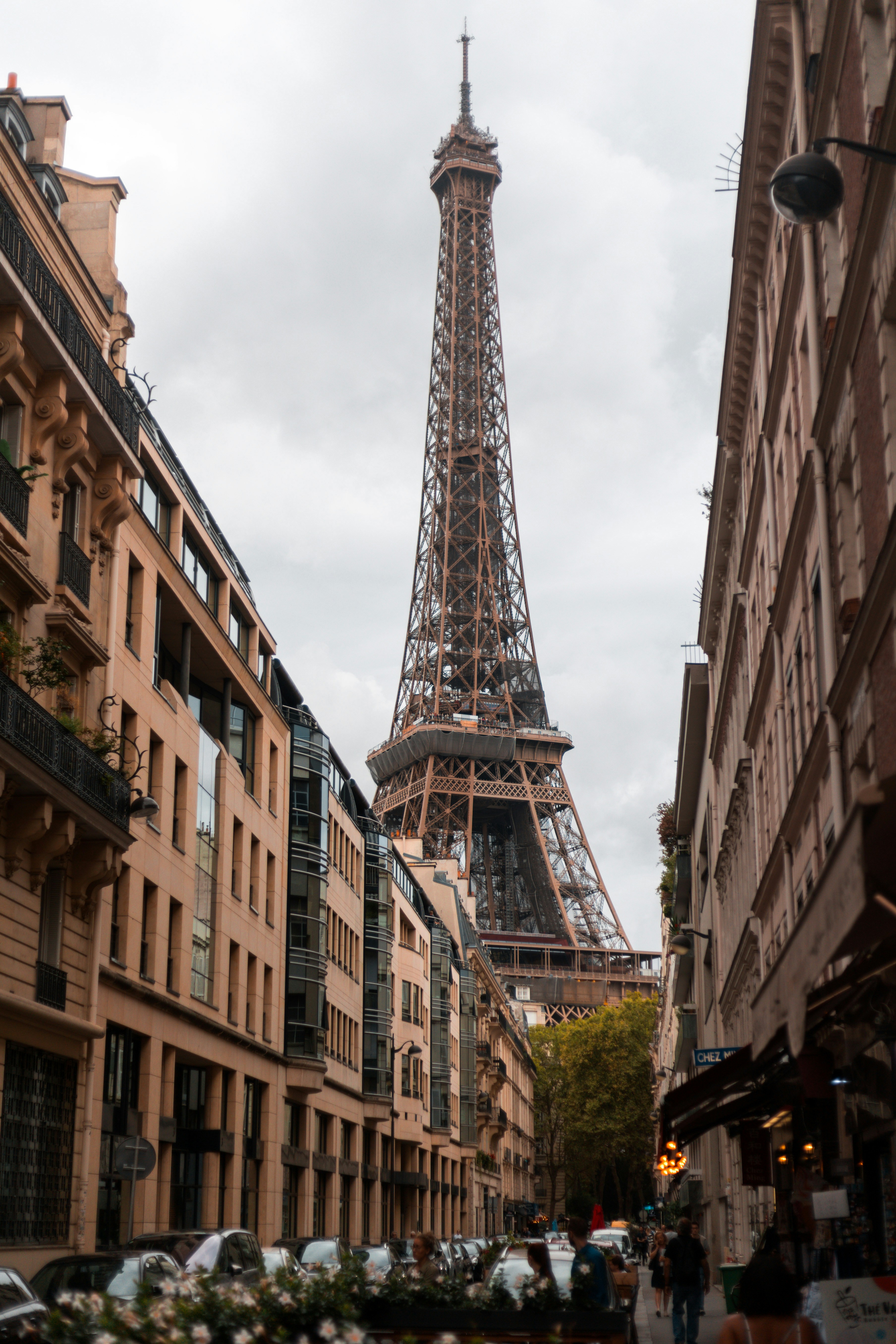 Eiffel Tower rises majestically above narrow Parisian streets lined with elegant buildings, capturing the essence of urban charm. A hint of autumn foliage adds warmth to the scene.