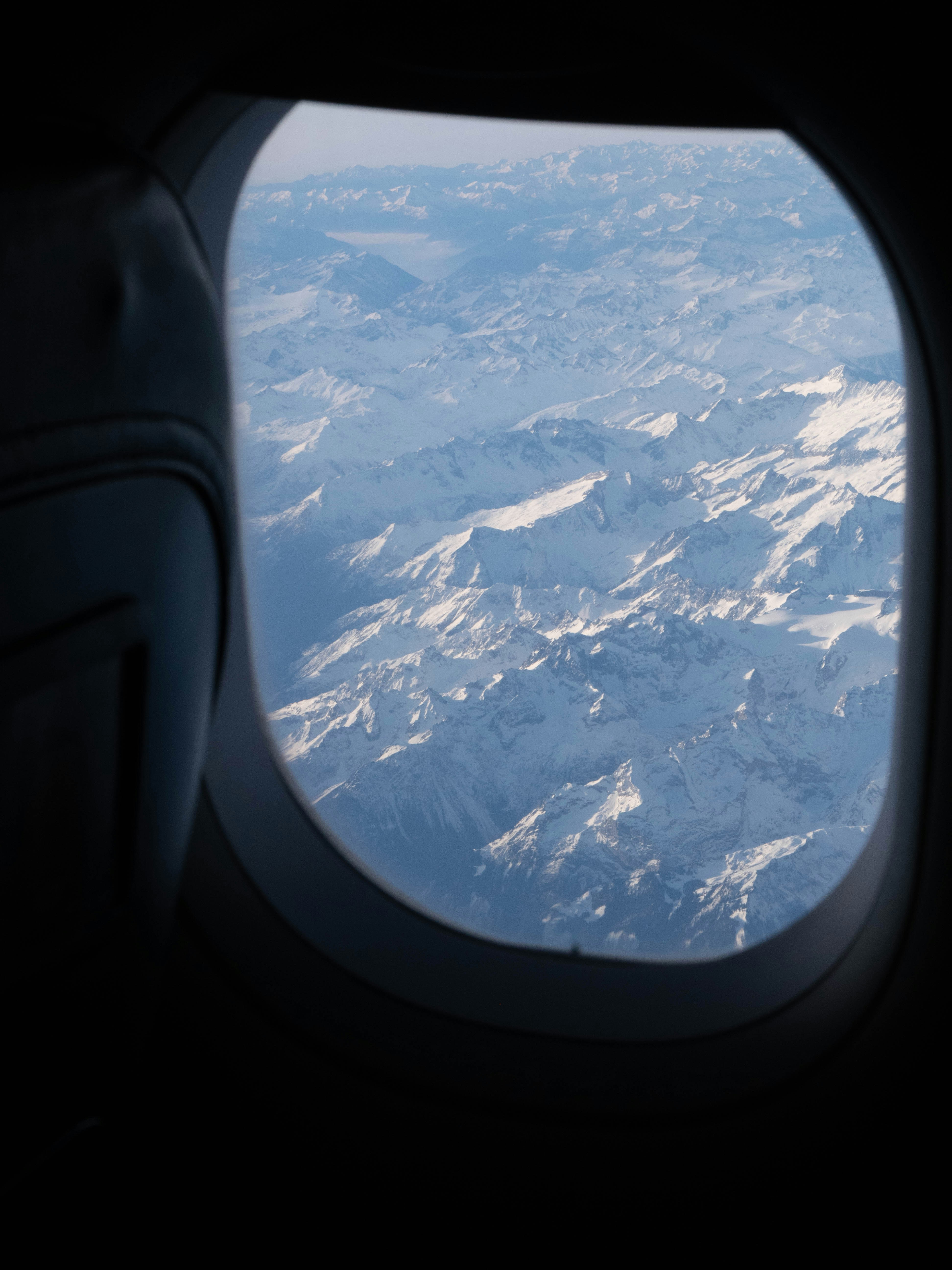 Snow-covered mountain ranges seen through an airplane window, framed by the aircraft's interior. A moment of tranquility high above the earth.
