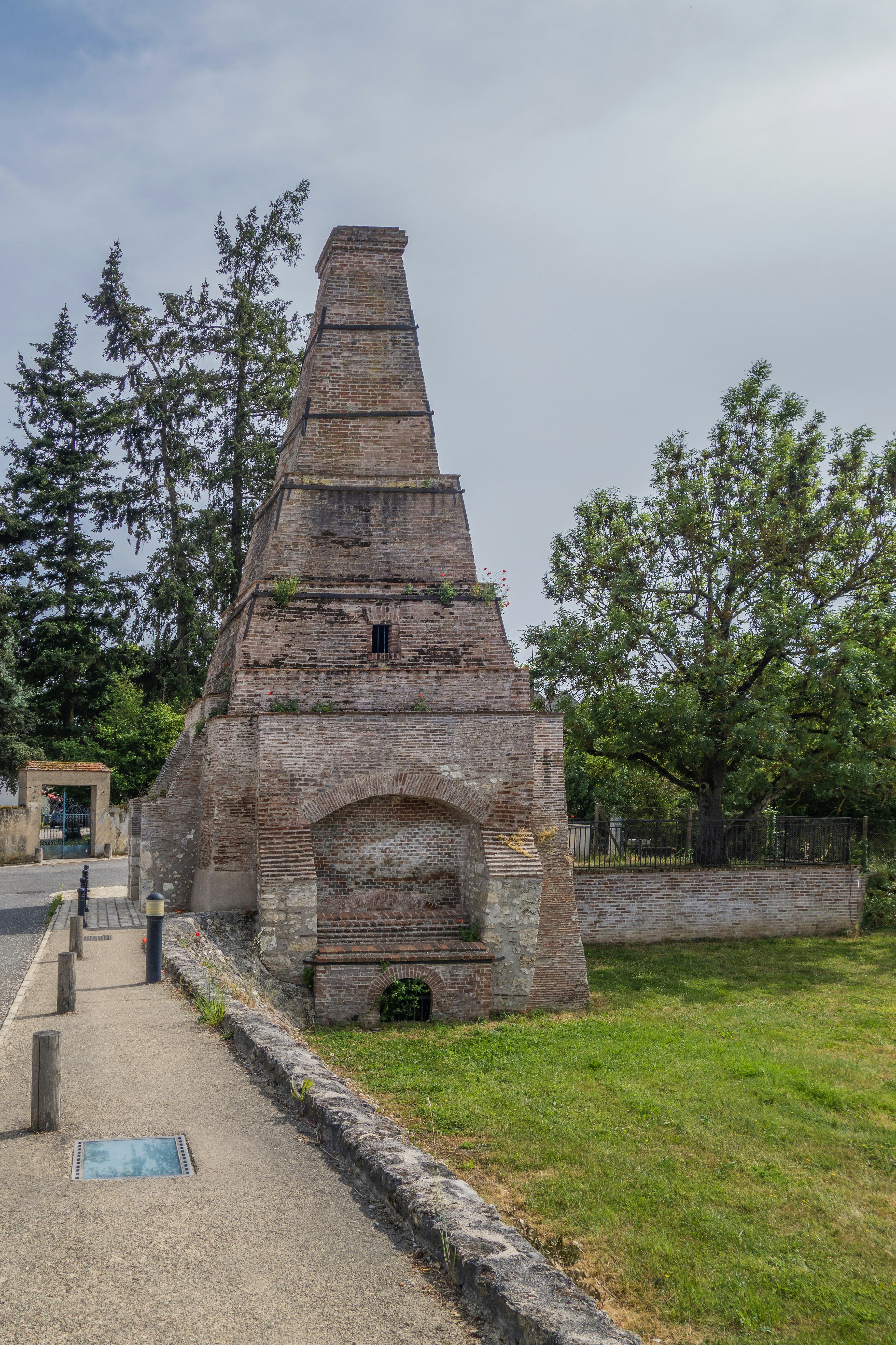 Ancient brick structure resembling a pyramid, adorned with greenery, set against a backdrop of trees and a clear sky.
