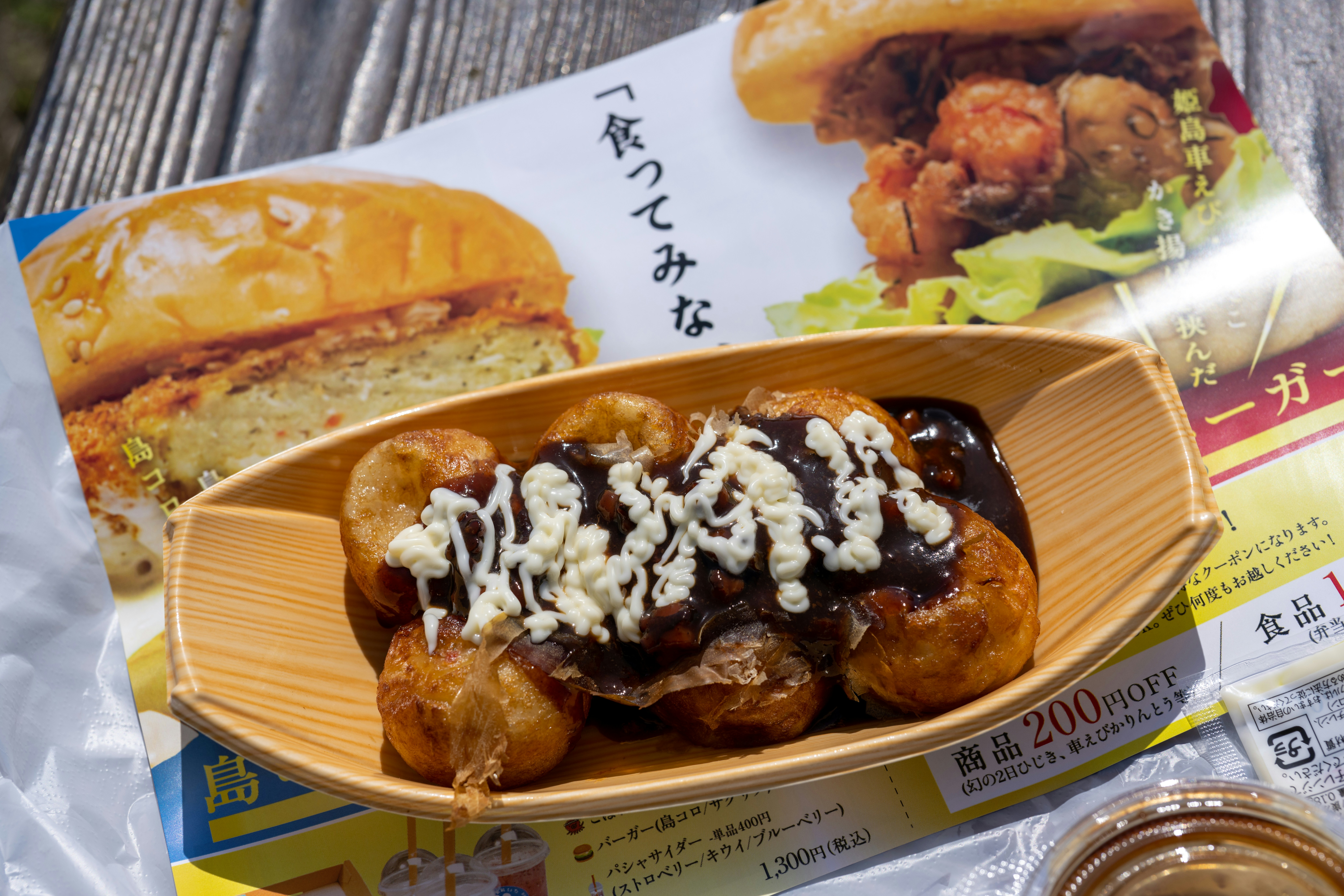 Takoyaki topped with sauce and mayonnaise served on a tray, with images of burgers in the background.