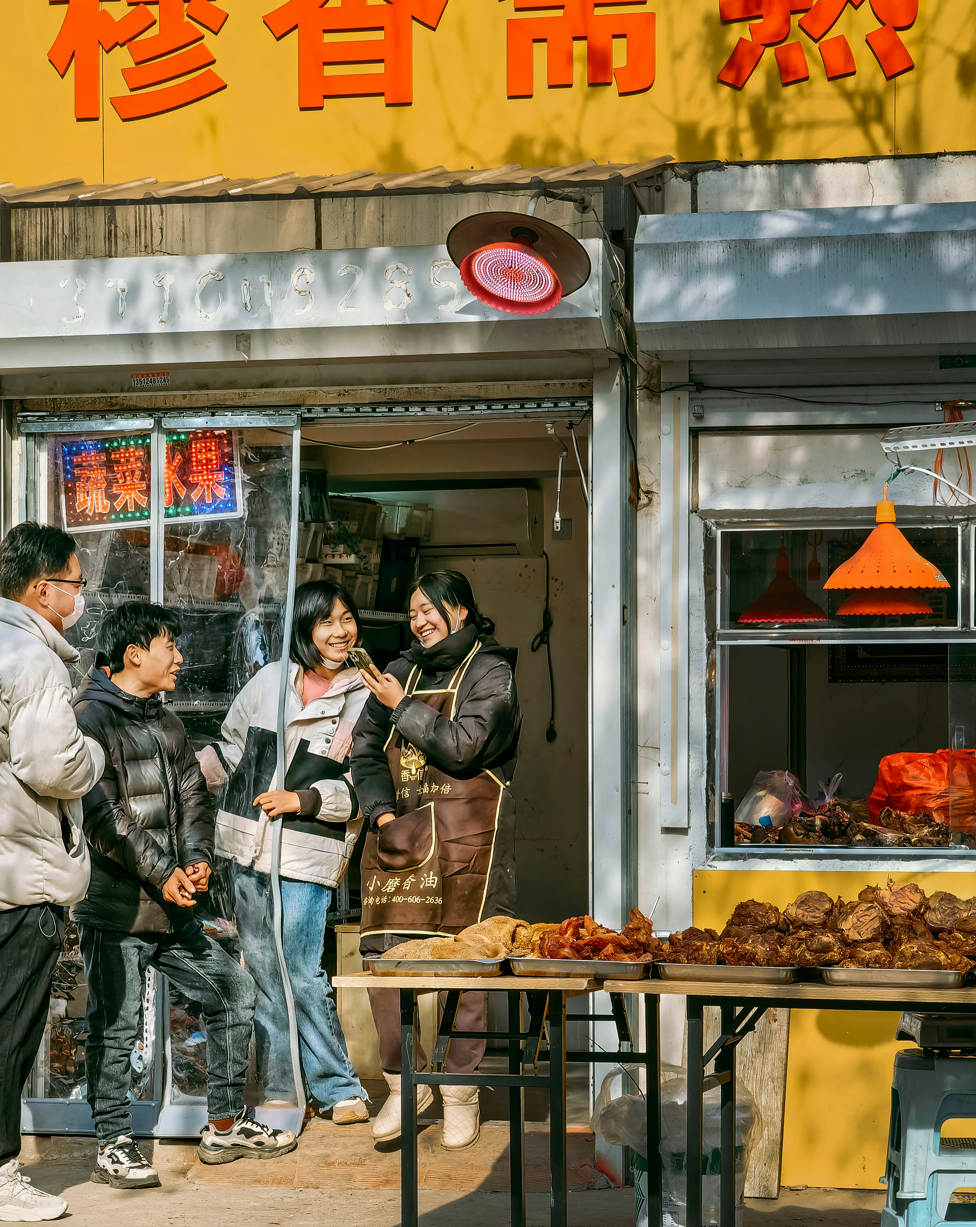 Street-side Moment: Friends Laugh by a Snack Stall Amid Golden Signage