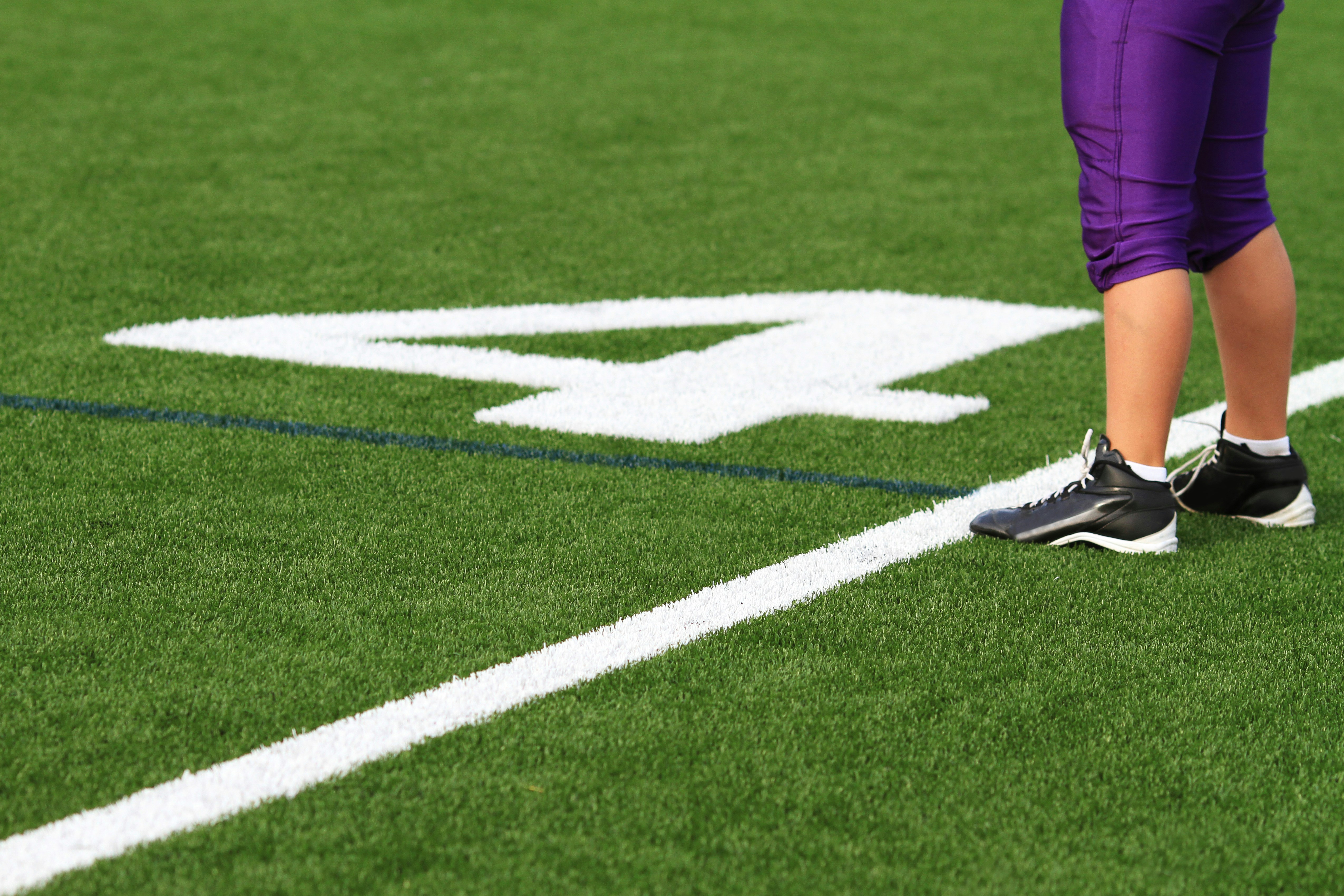 Athlete in purple shorts standing next to a white yard marker on artificial turf, preparing for the next play.