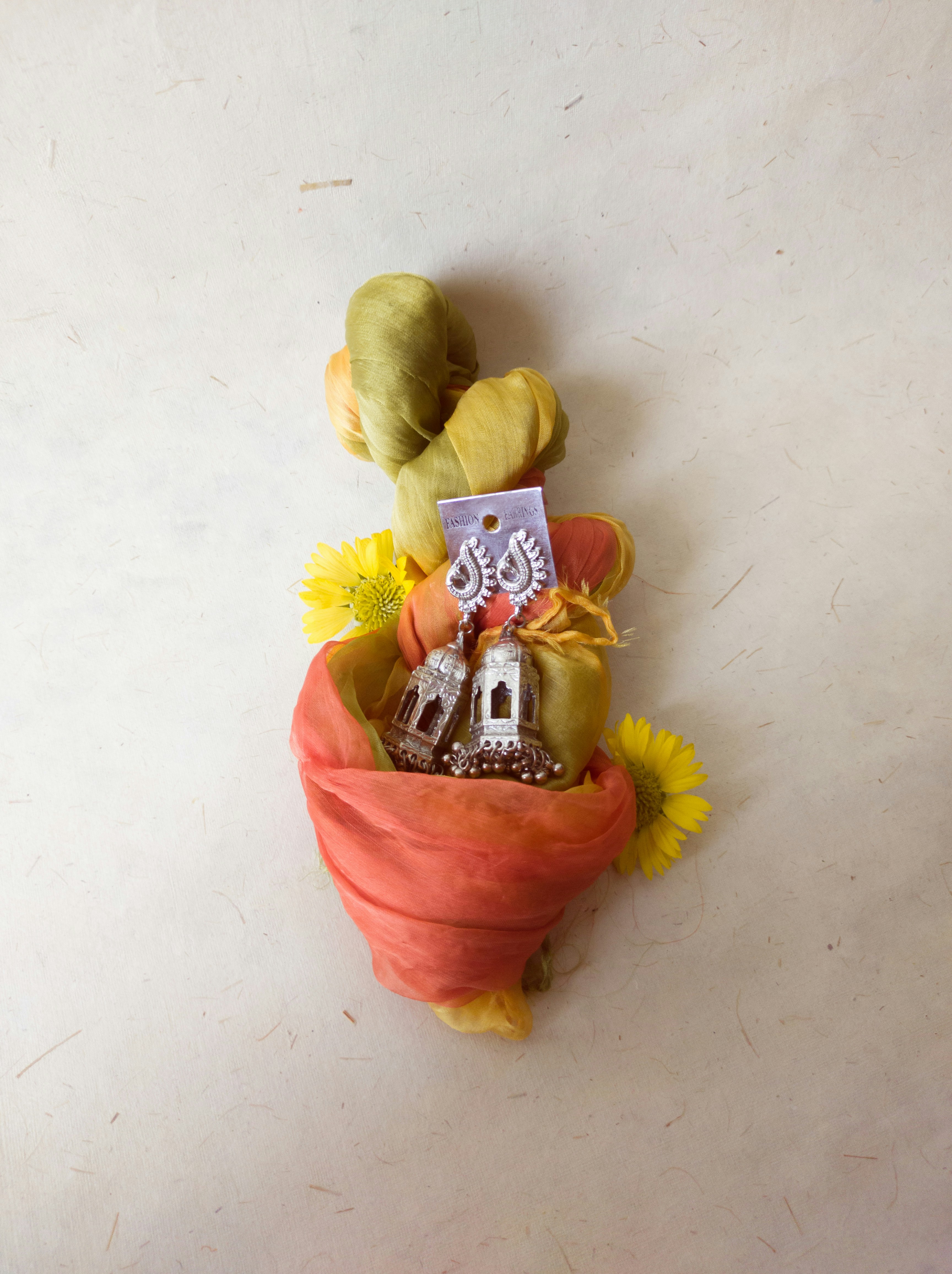Handcrafted floral talisman with yellow daisies and silver charms wrapped in coral scarf