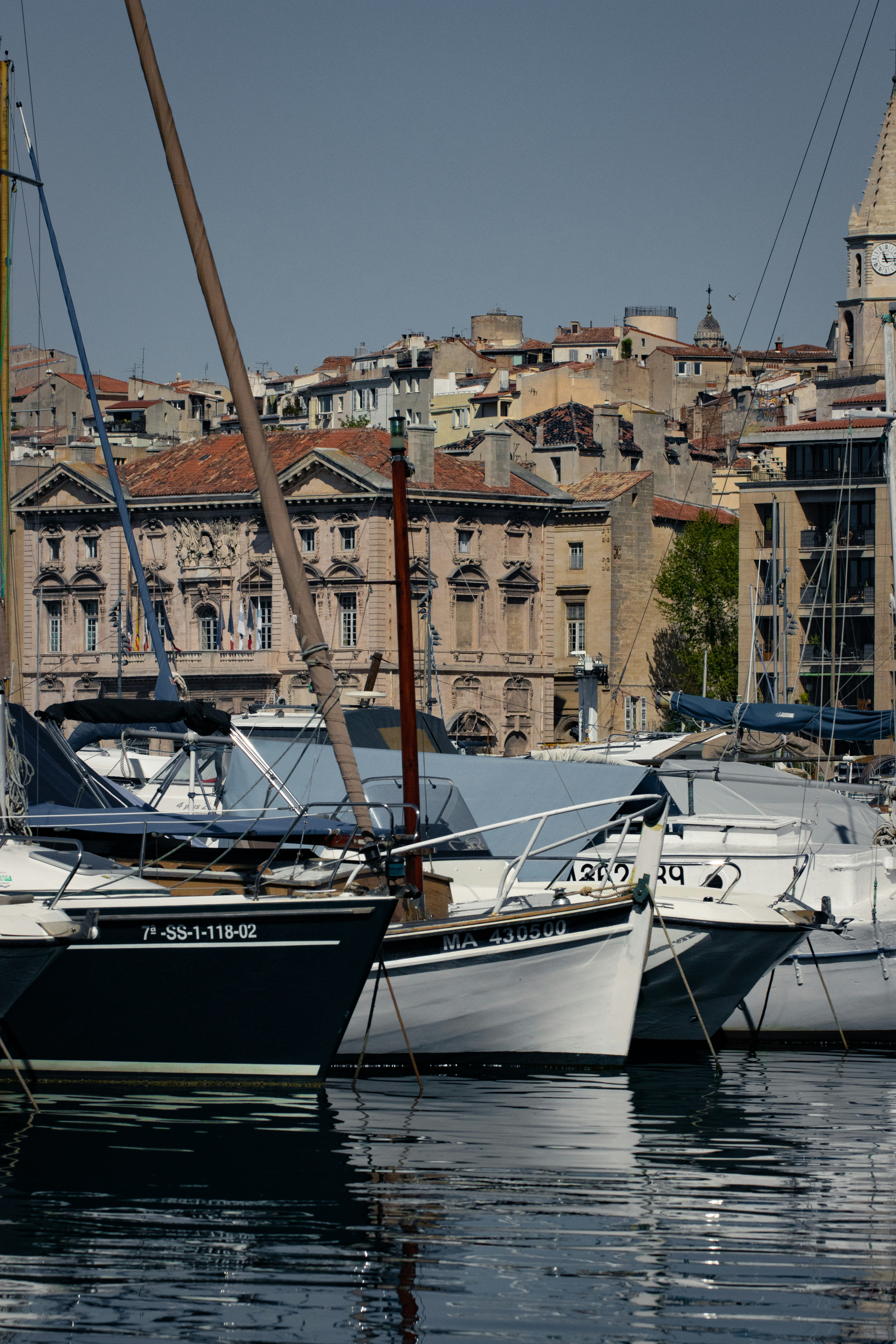 Harbor of Echoes: Sailboats, dark masts, and sunlit facades along a historic waterfront