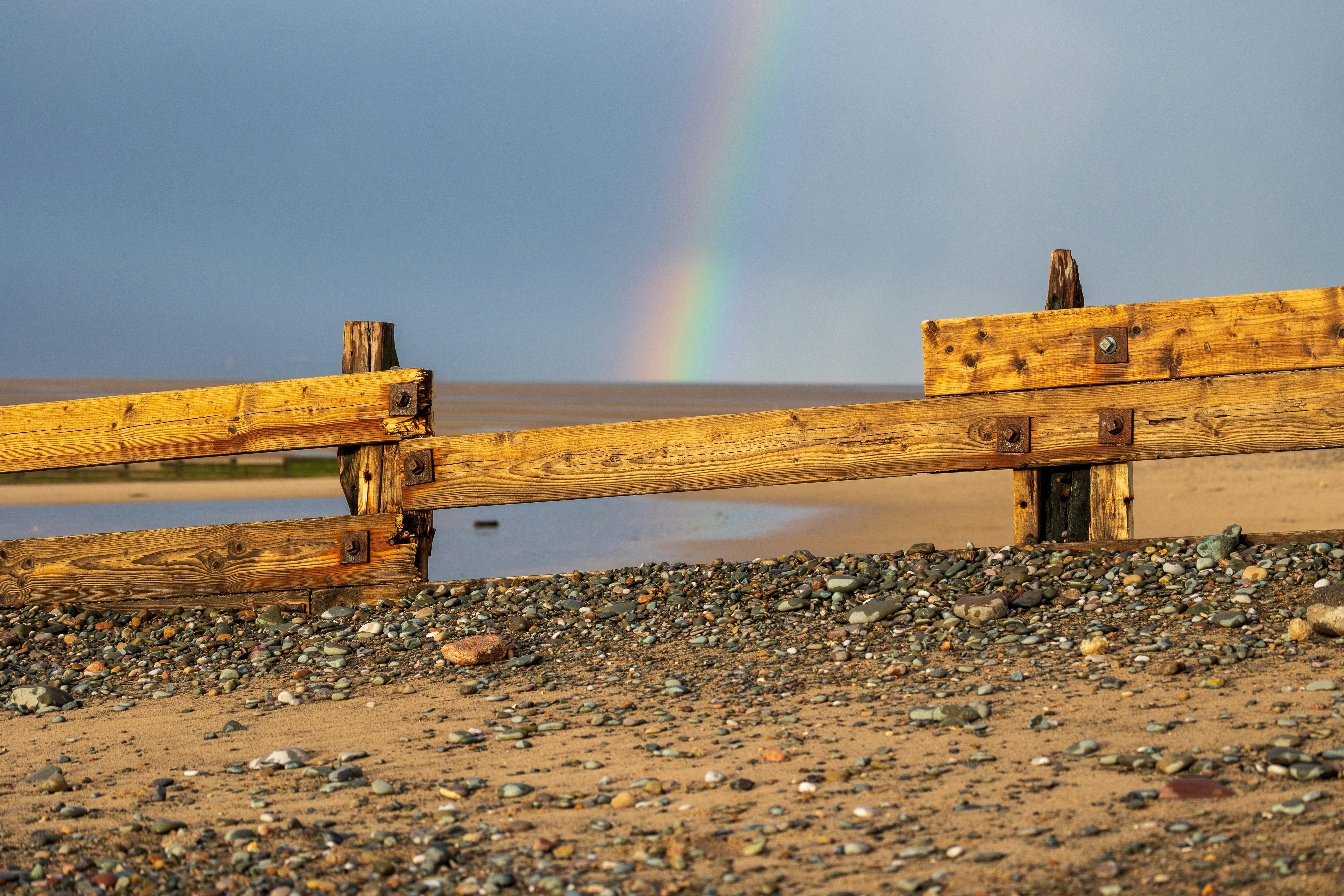 Rainbow Over Weathered Rails: A Seaside Fence Amid Pebbled Shore