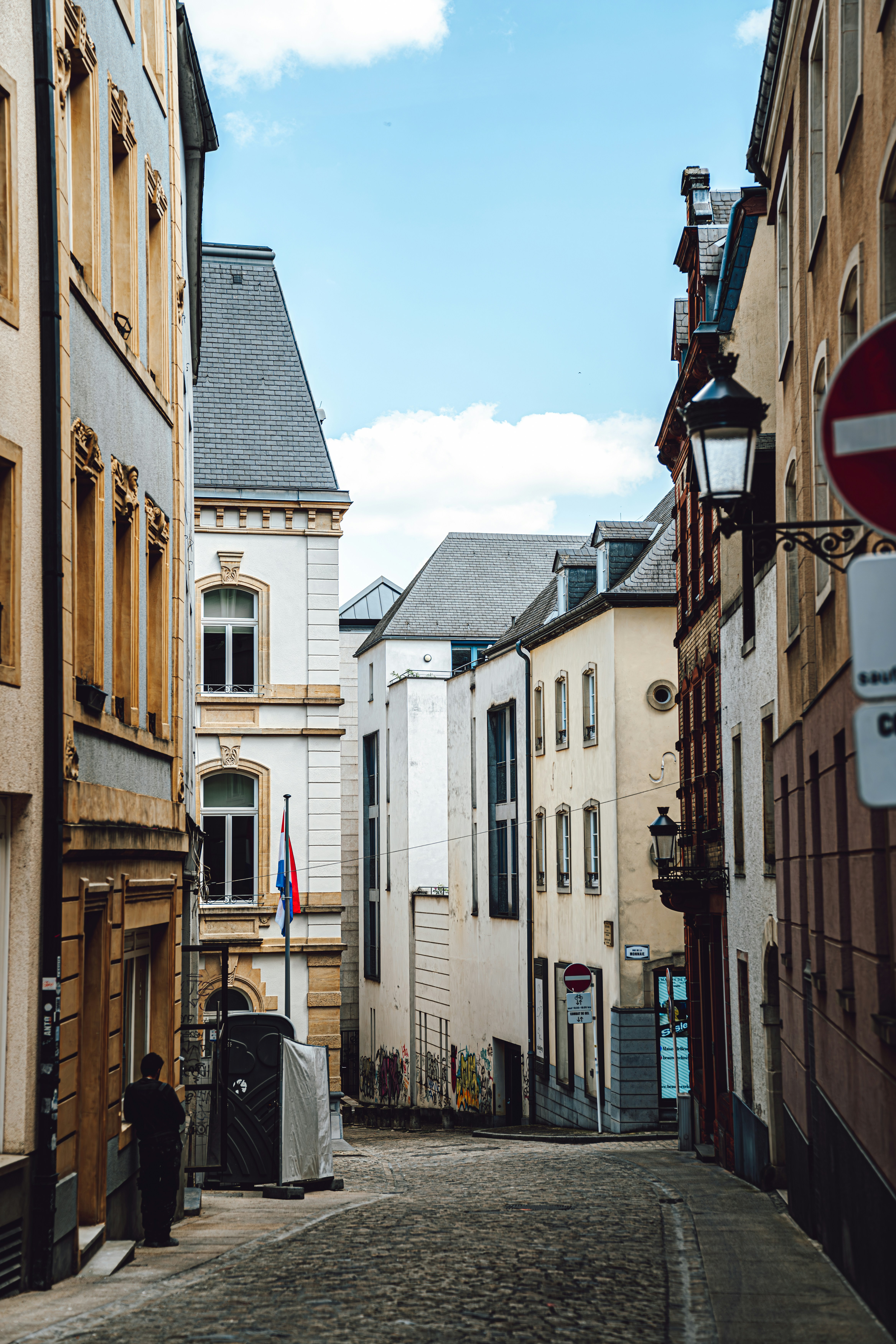 Charming alleyway flanked by historic buildings, showcasing a blend of architectural styles and a hint of modernity. A flag flutters gently in the breeze.