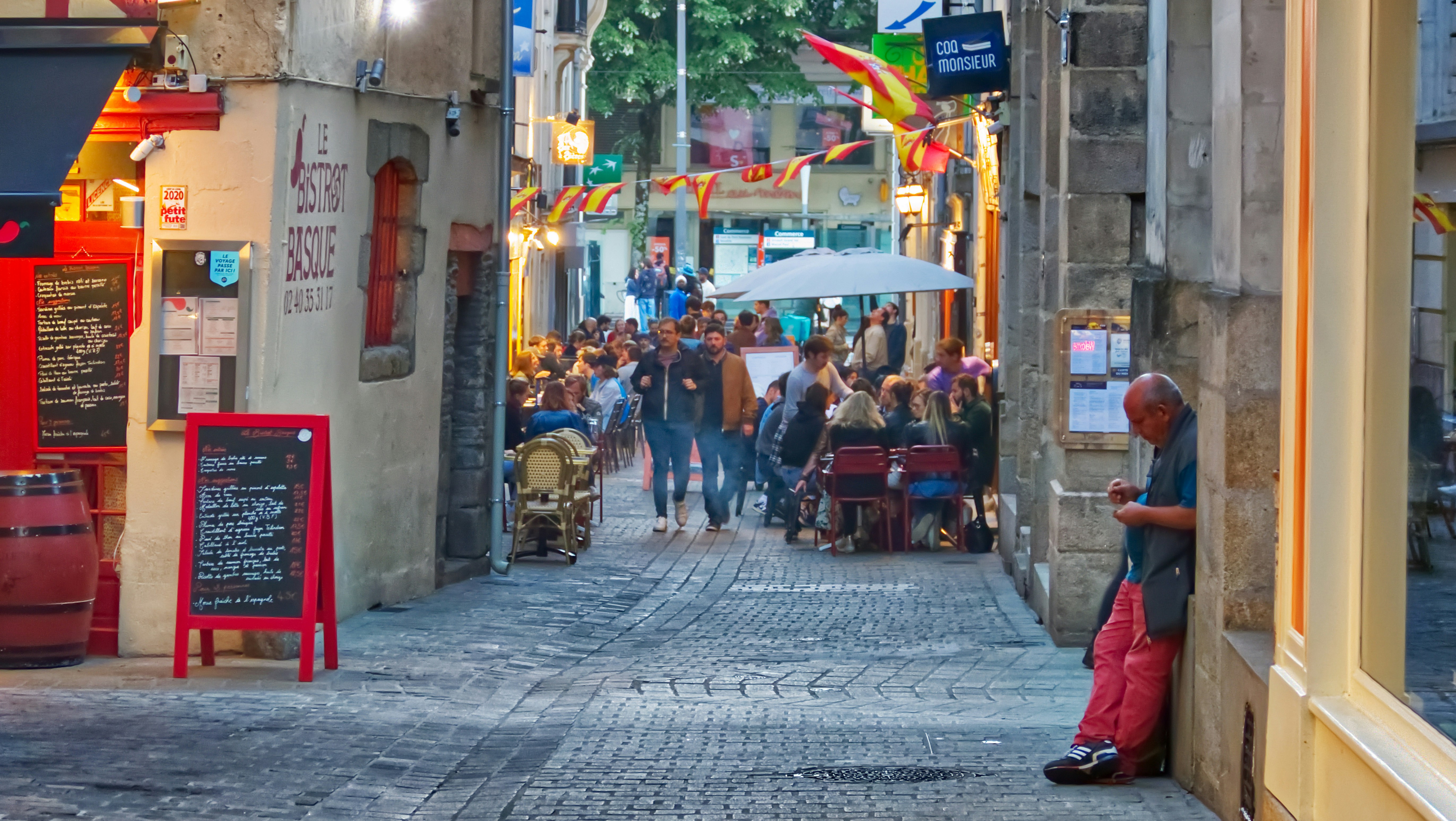 Cobbled Street, Lanterns, and a Quiet Stranger in a Lively European Alley