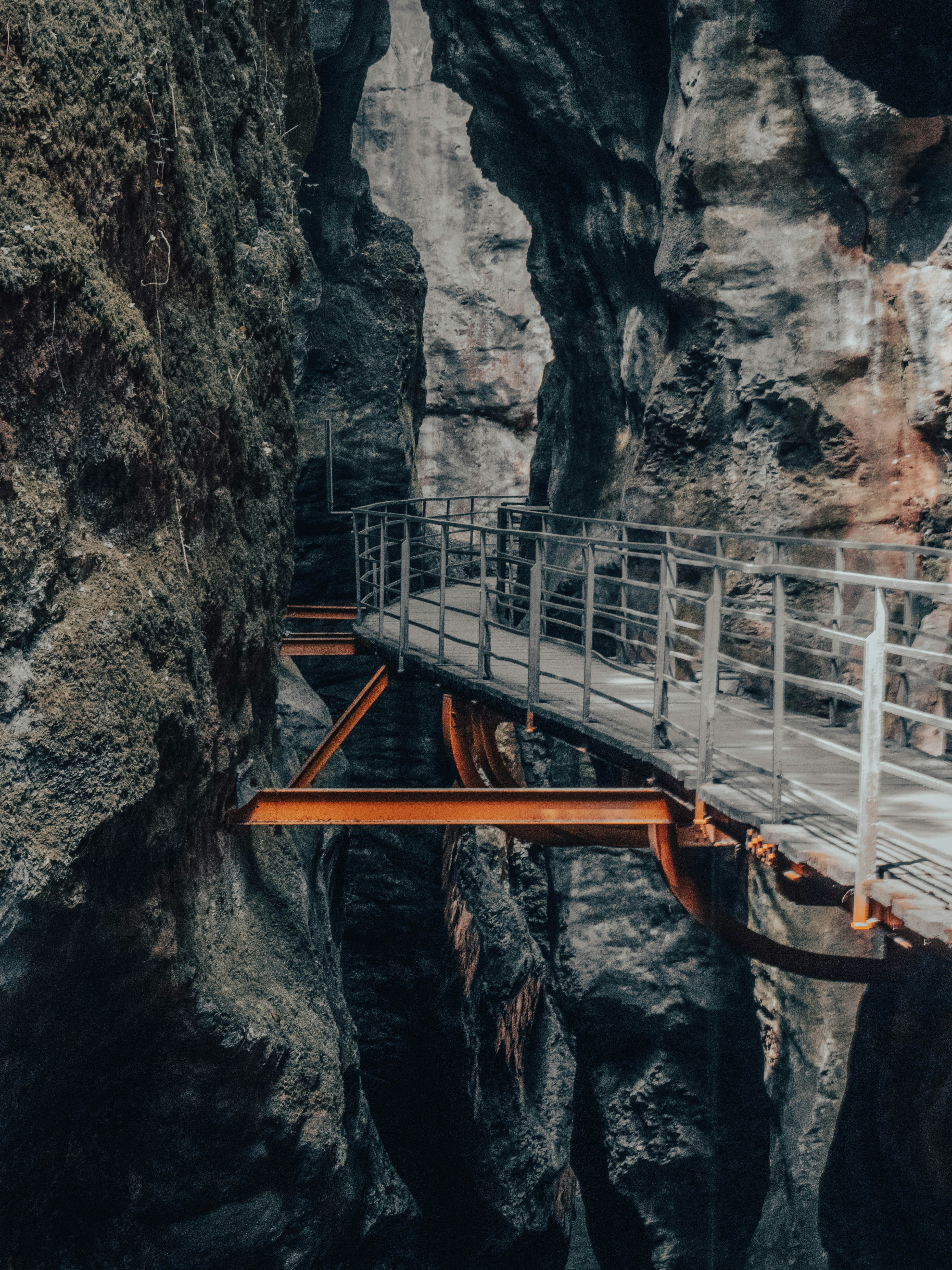 Narrow metal walkway suspended between towering rock formations in a cavernous gorge.
