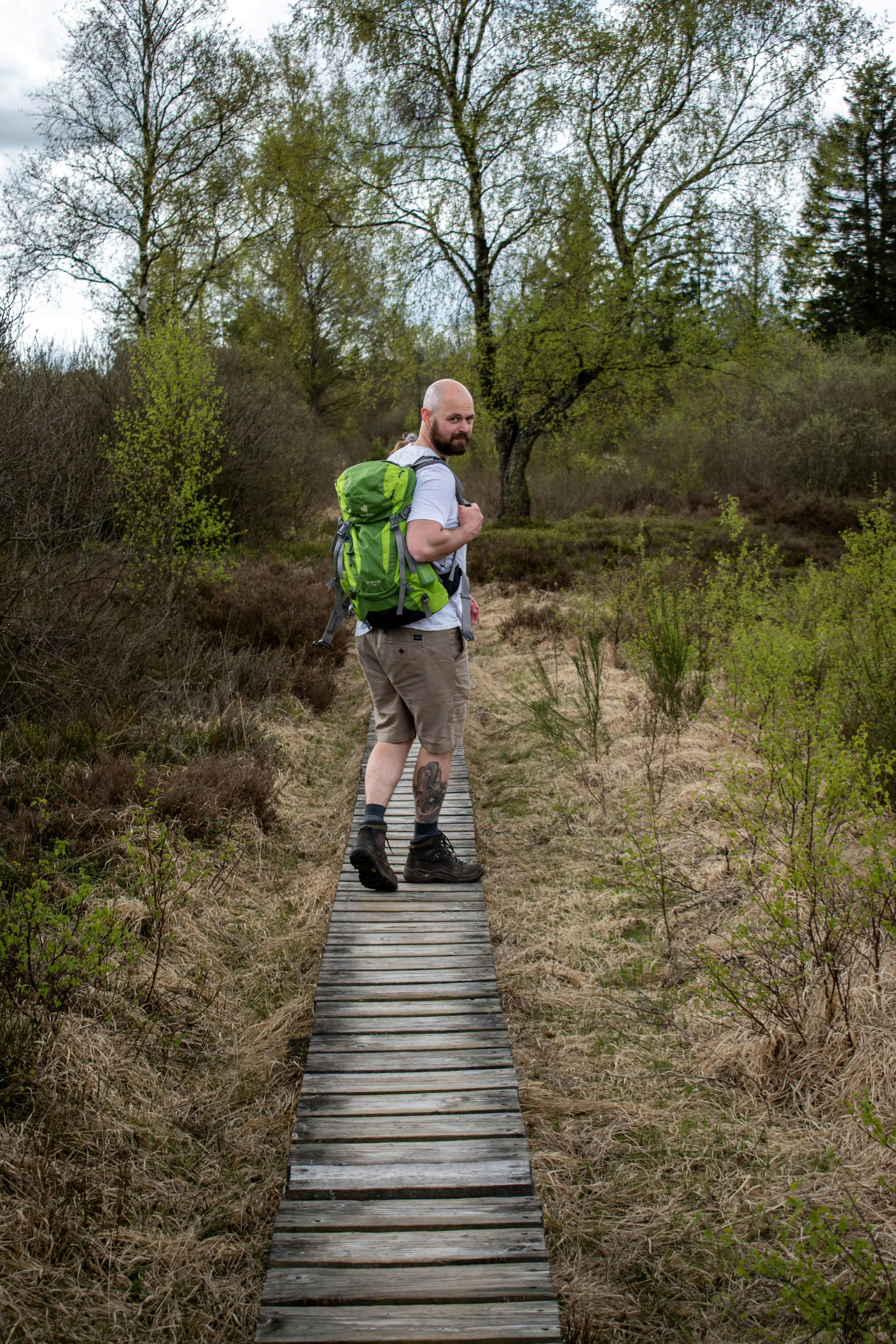 Green-Backpack Hiker on a Narrow Boardwalk Through Scrubland