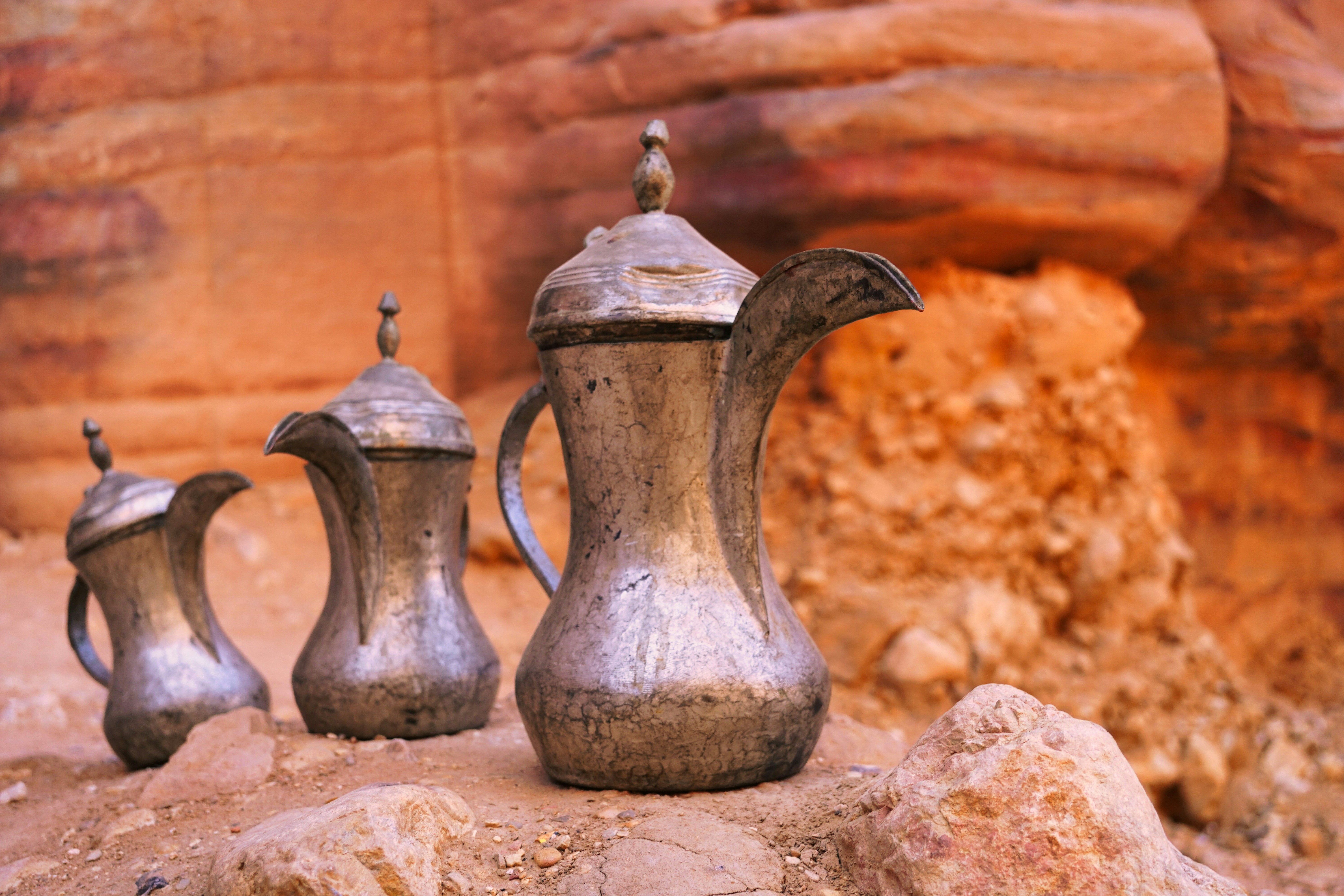 A group of three metal pitchers sitting on top of a rock photo – Free ...