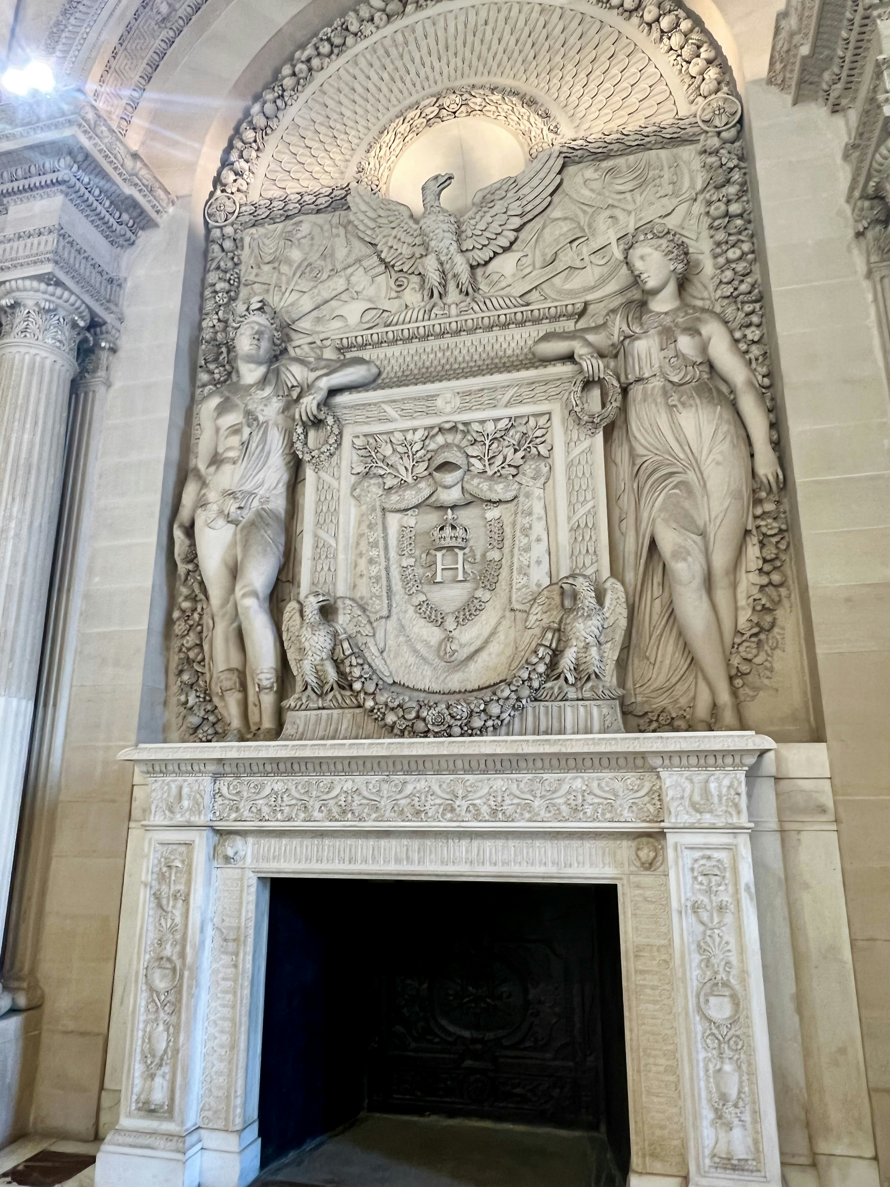 An ornate marble fireplace mantle features a high-relief heraldic scene with an eagle atop a central shield, flanked by two statues.