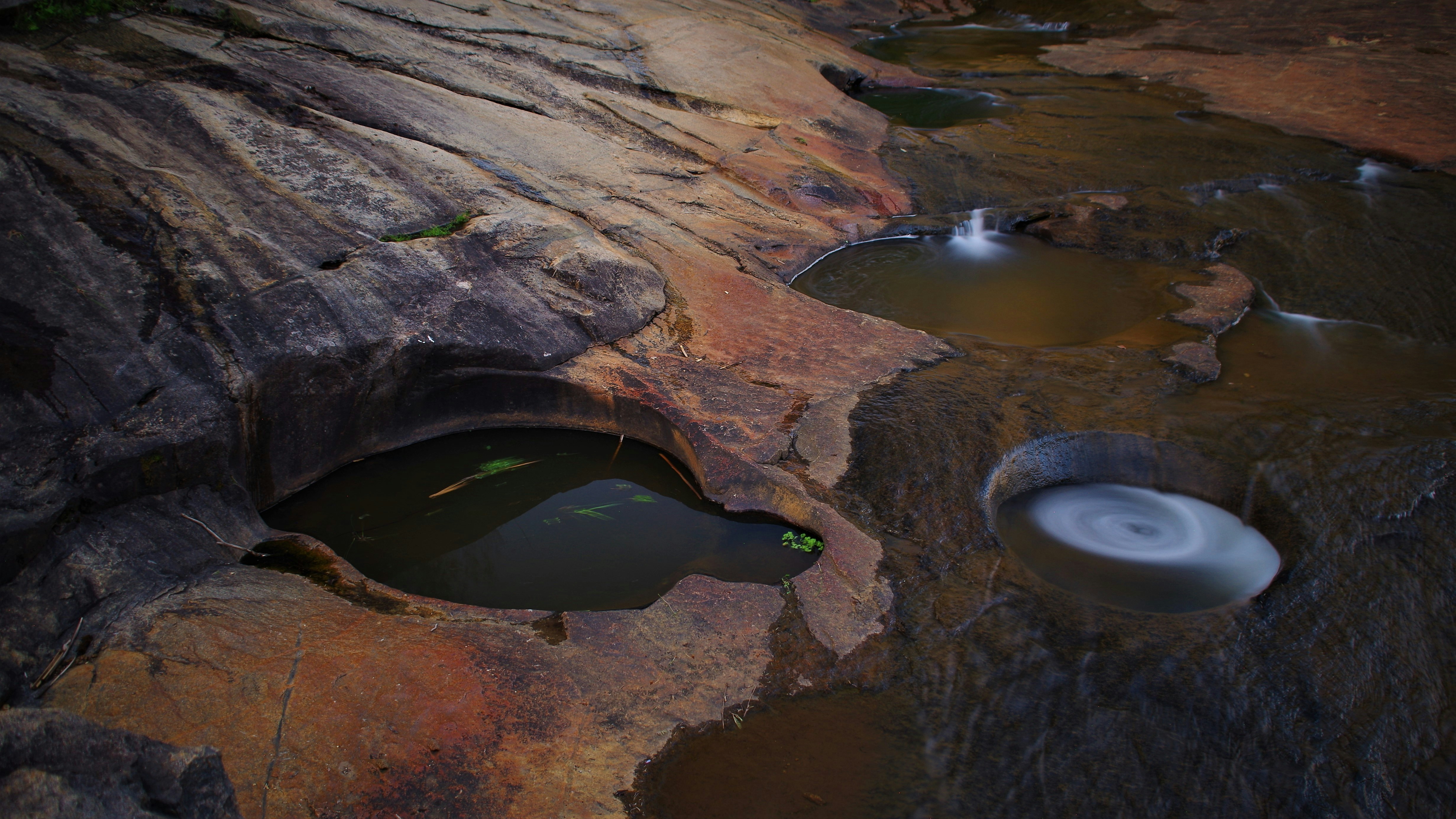 Smooth stones with swirling water pools and lush greenery on rugged terrain.