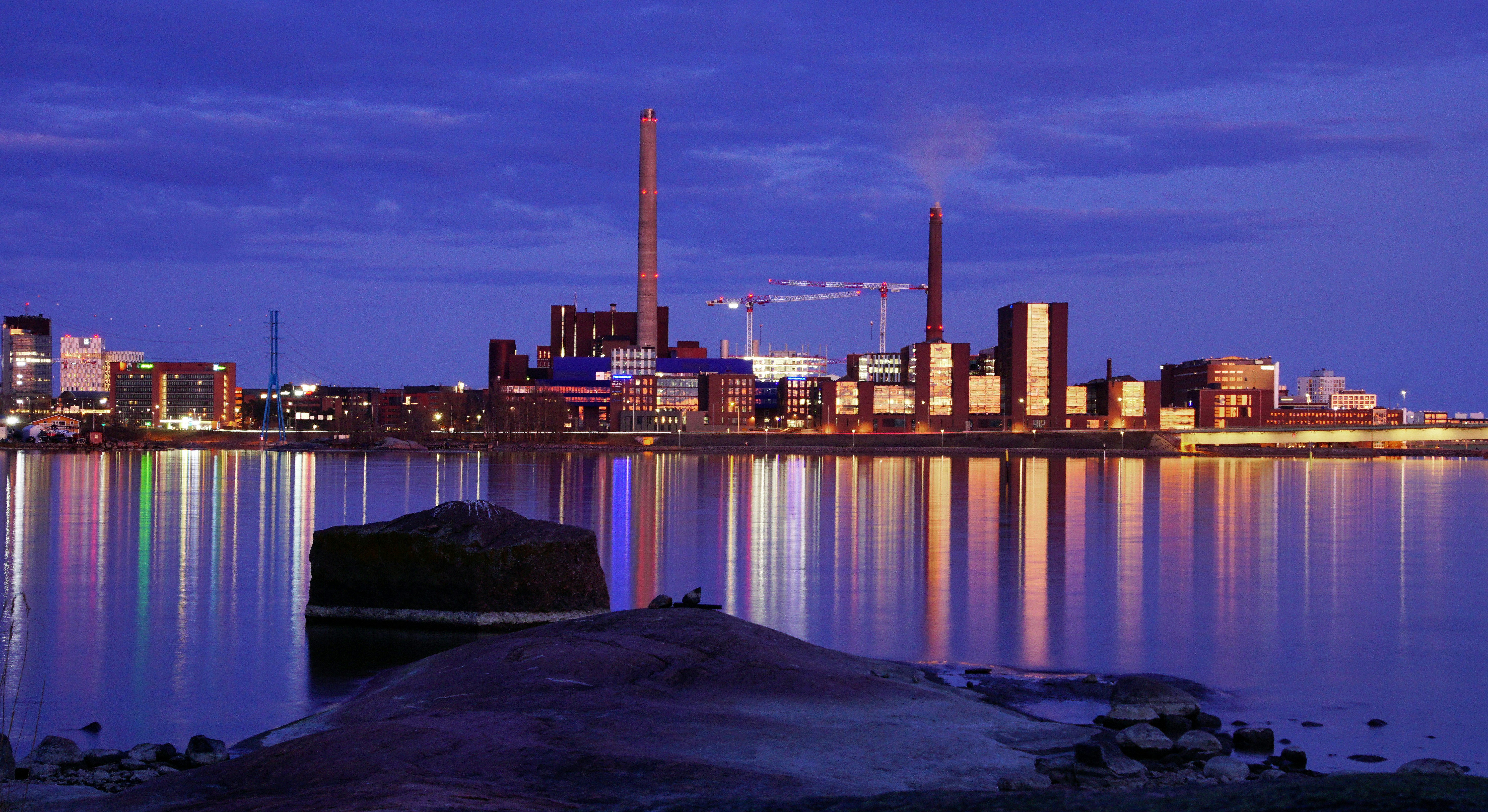 Industrial glow across the river: refinery towers and cityscape at dusk